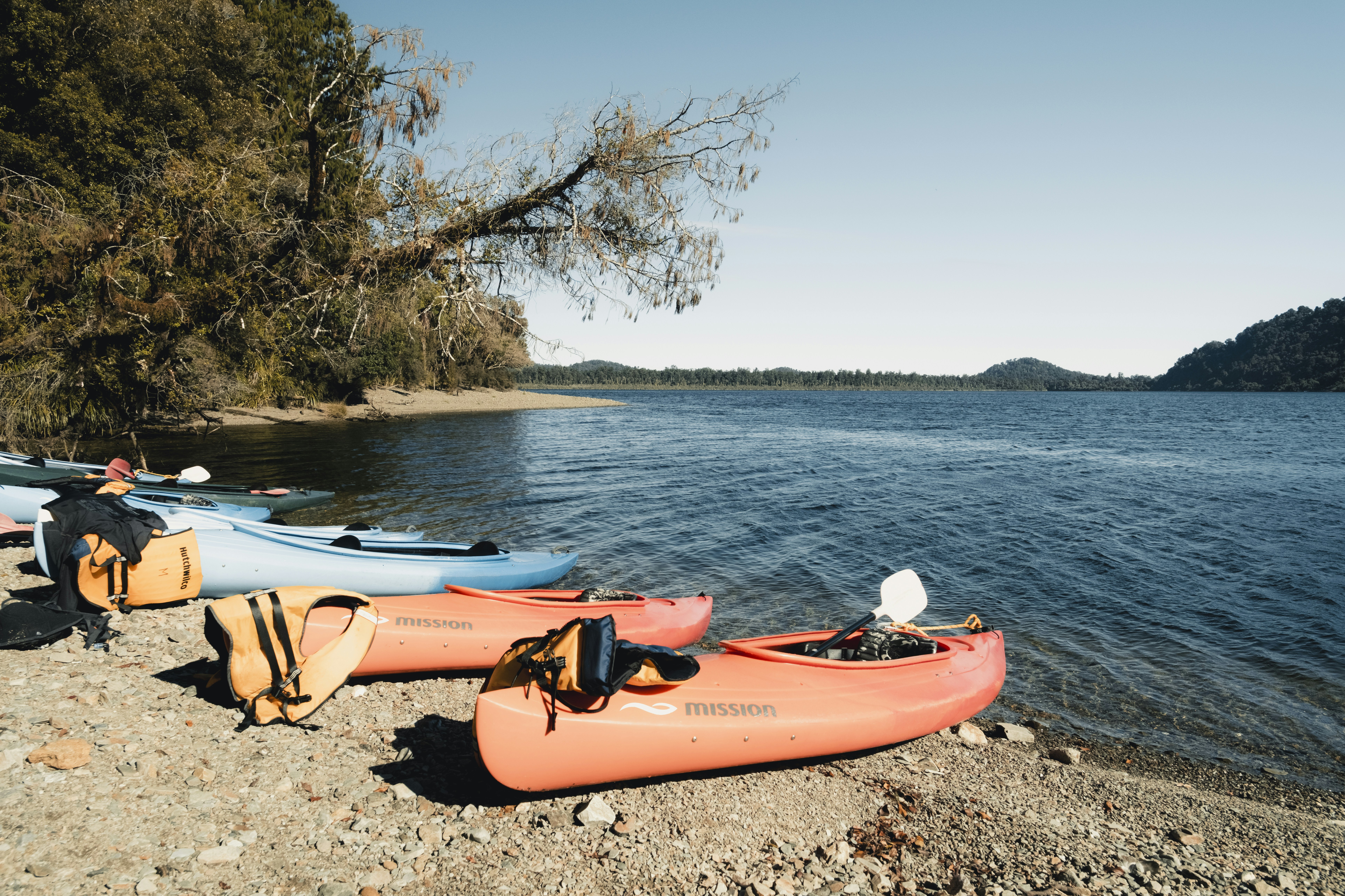 Colorful Kayaks Rest Along a Pebble Shore Under a Calm Blue Sky