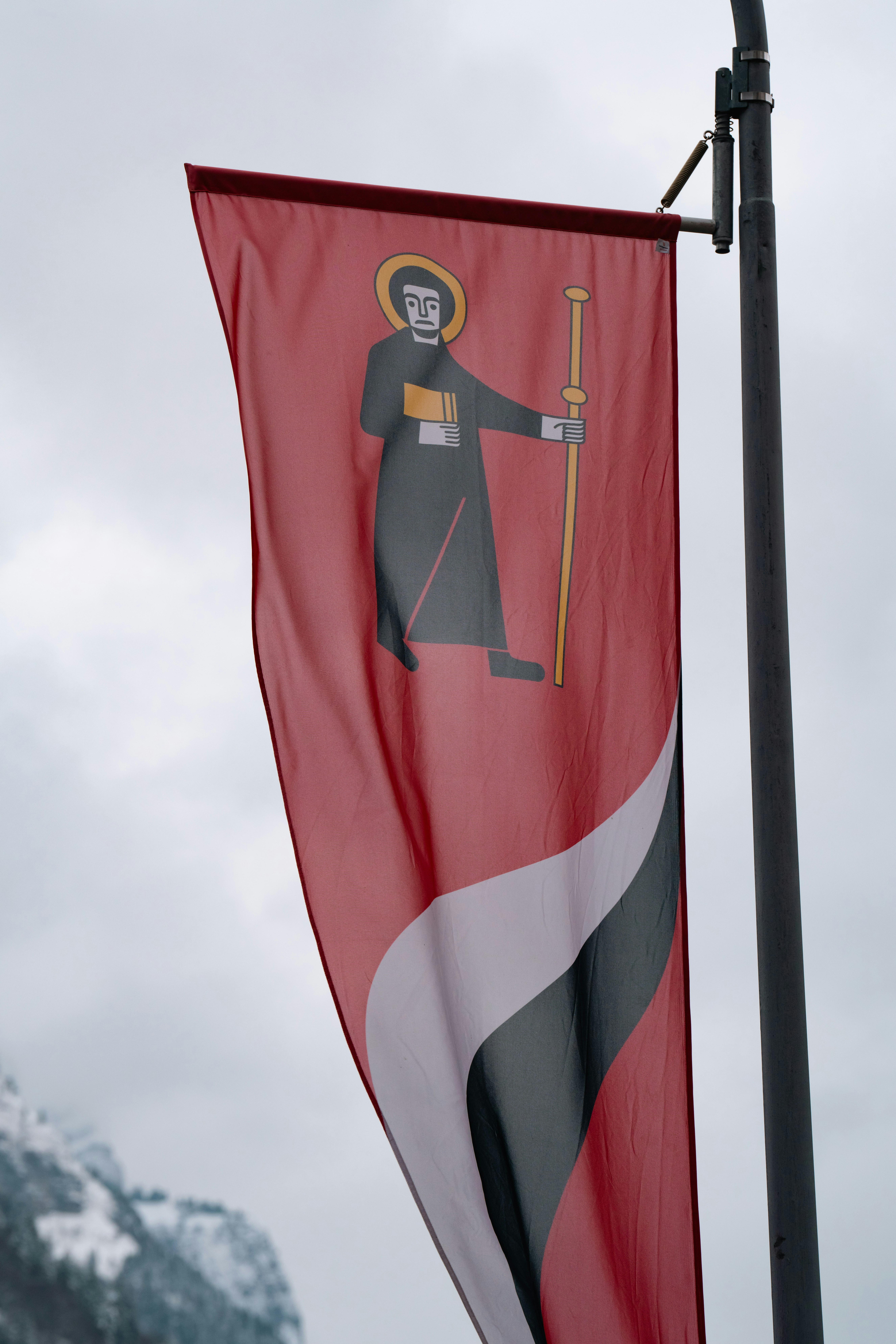 Red banner with saintly figure and staff fluttering beside a tall pole