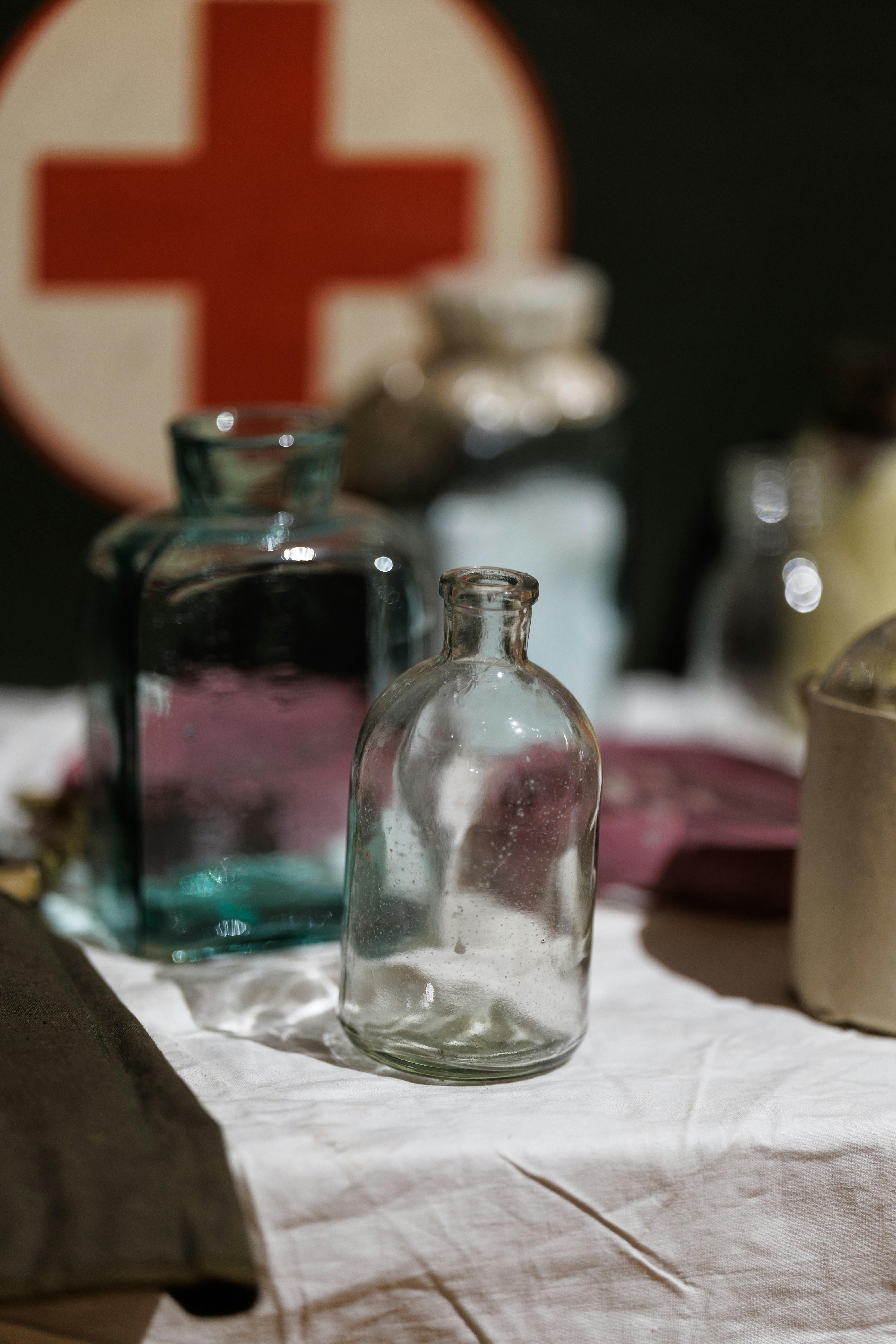 Tiny Glass Bottles on a Table: A Still Life with a Red Cross Emblem