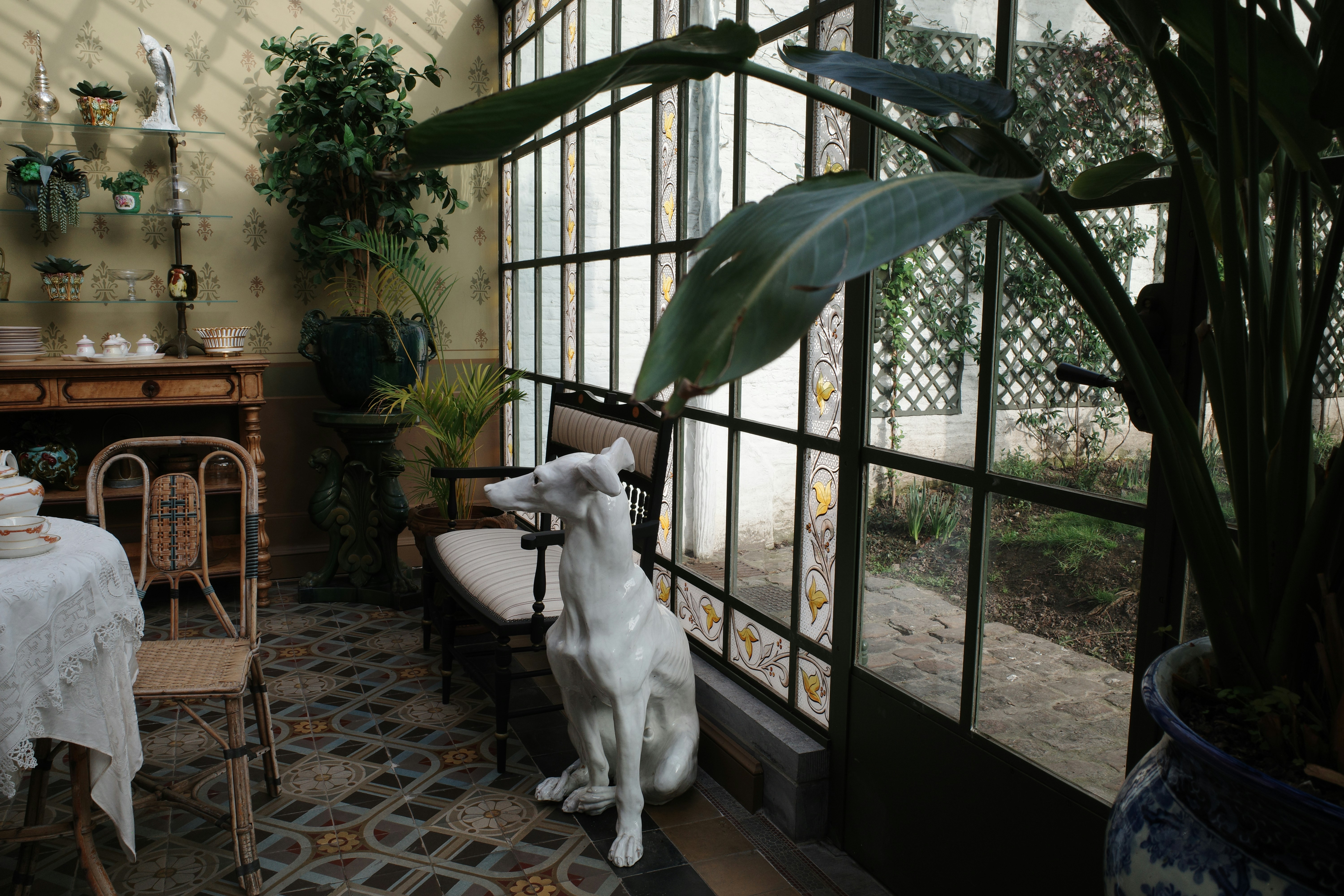 Elegant porcelain and a seated statue in a sunlit conservatory cafe