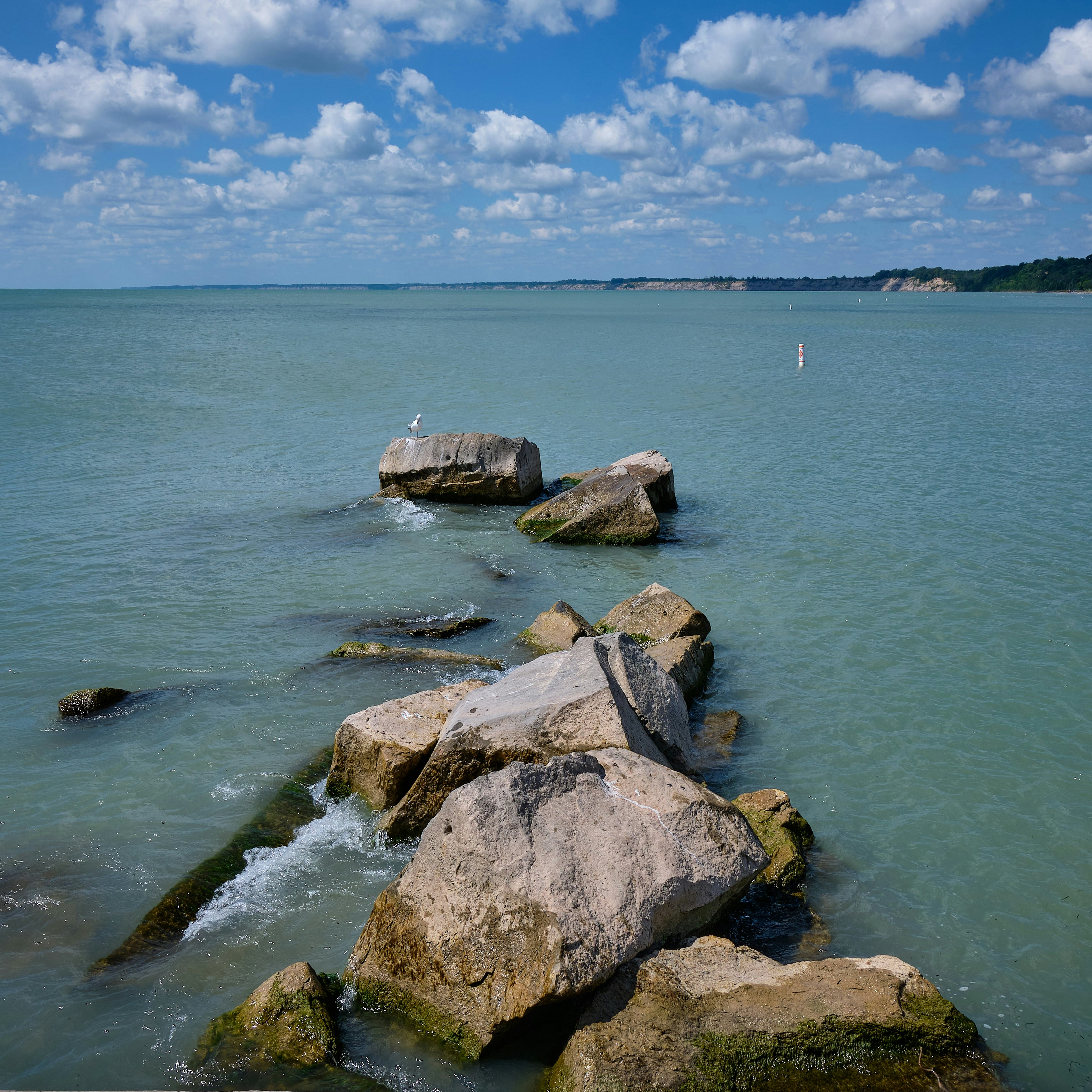 Rocks Reaching into Calm Blue Water under a Sky of Puffs
