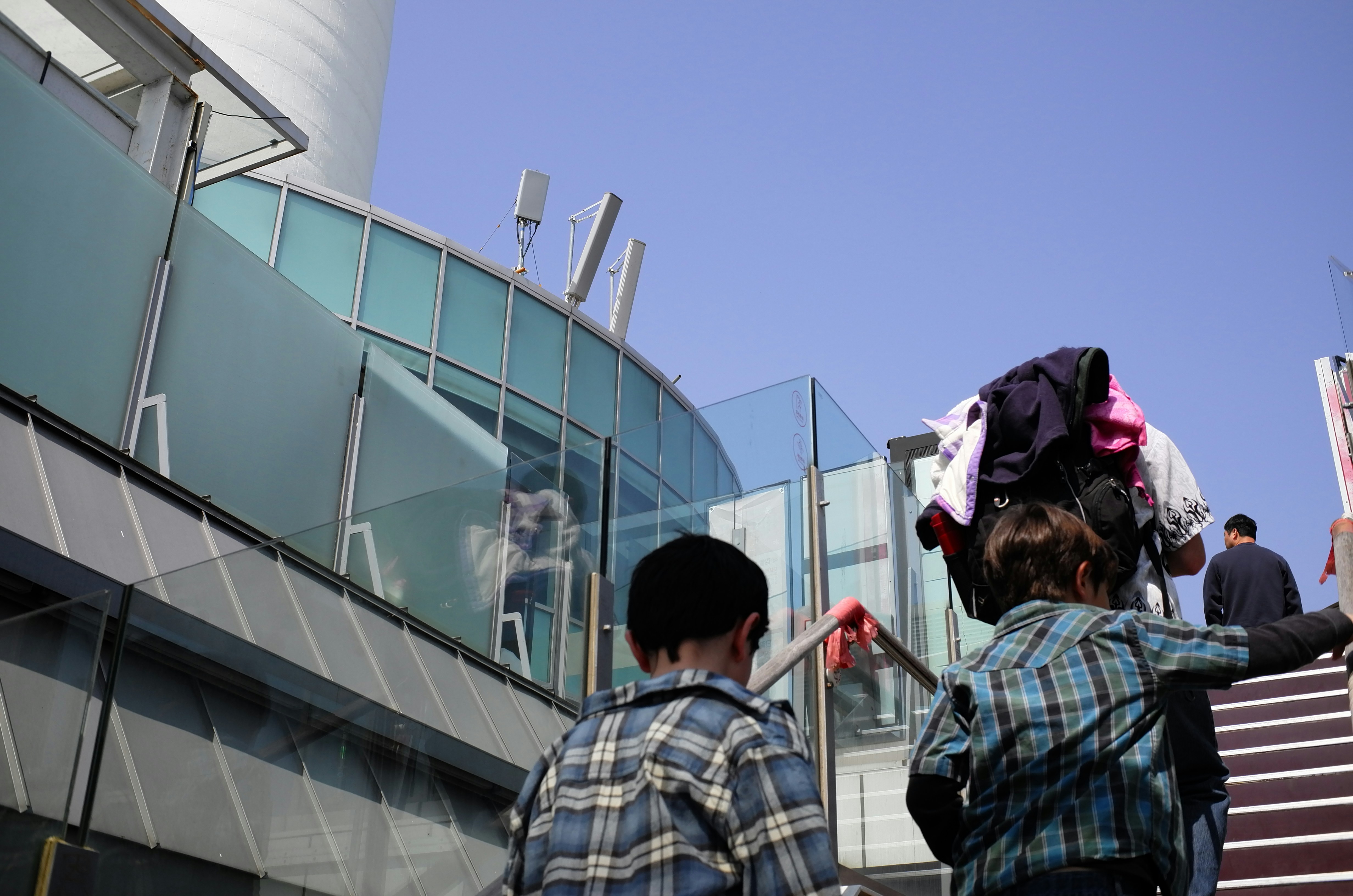 Ascending Light: Tourists Climb for a View at a Modern Glass Corridor
