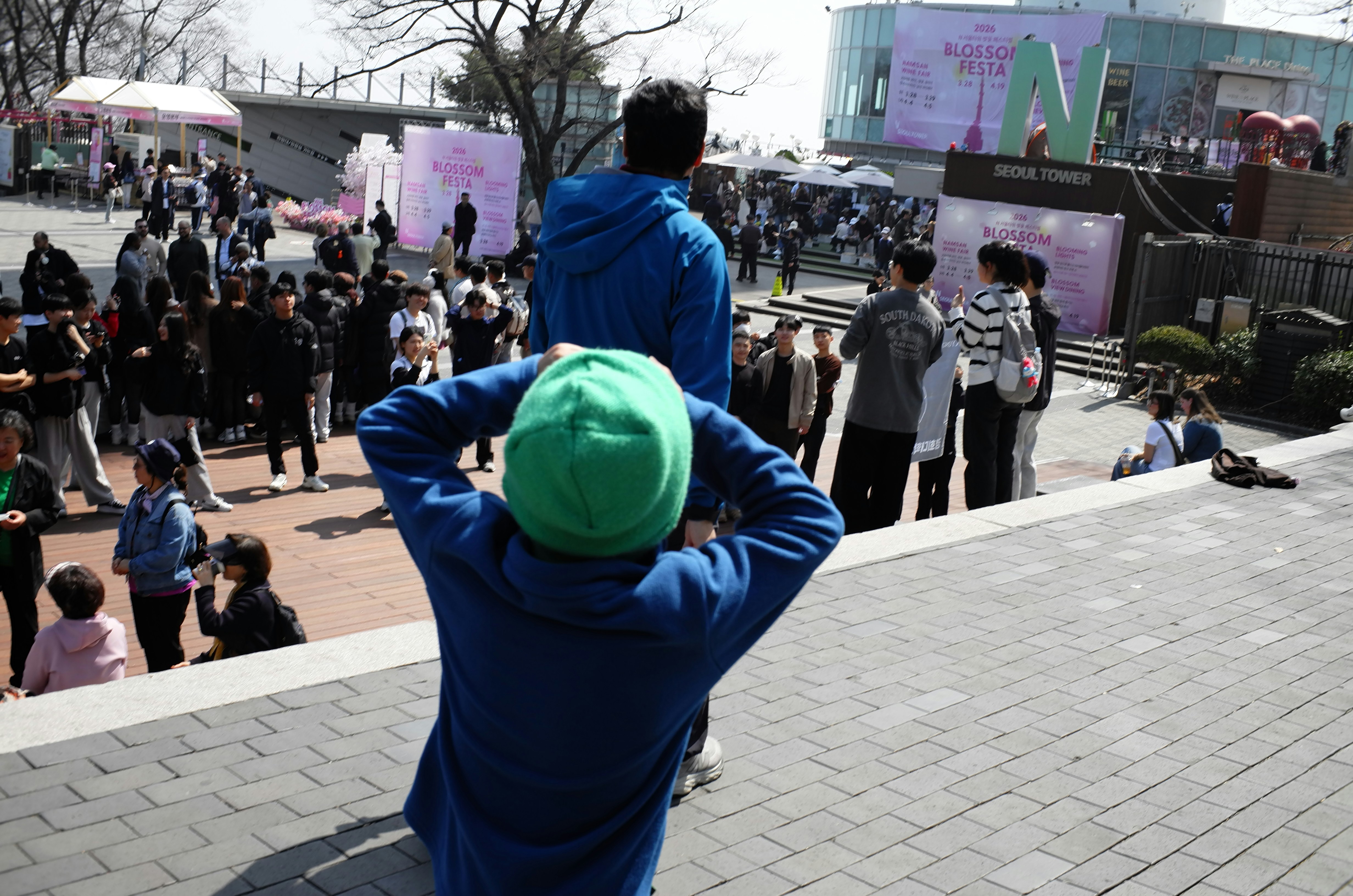 Blue-hooded climber watches a crowd from the plaza