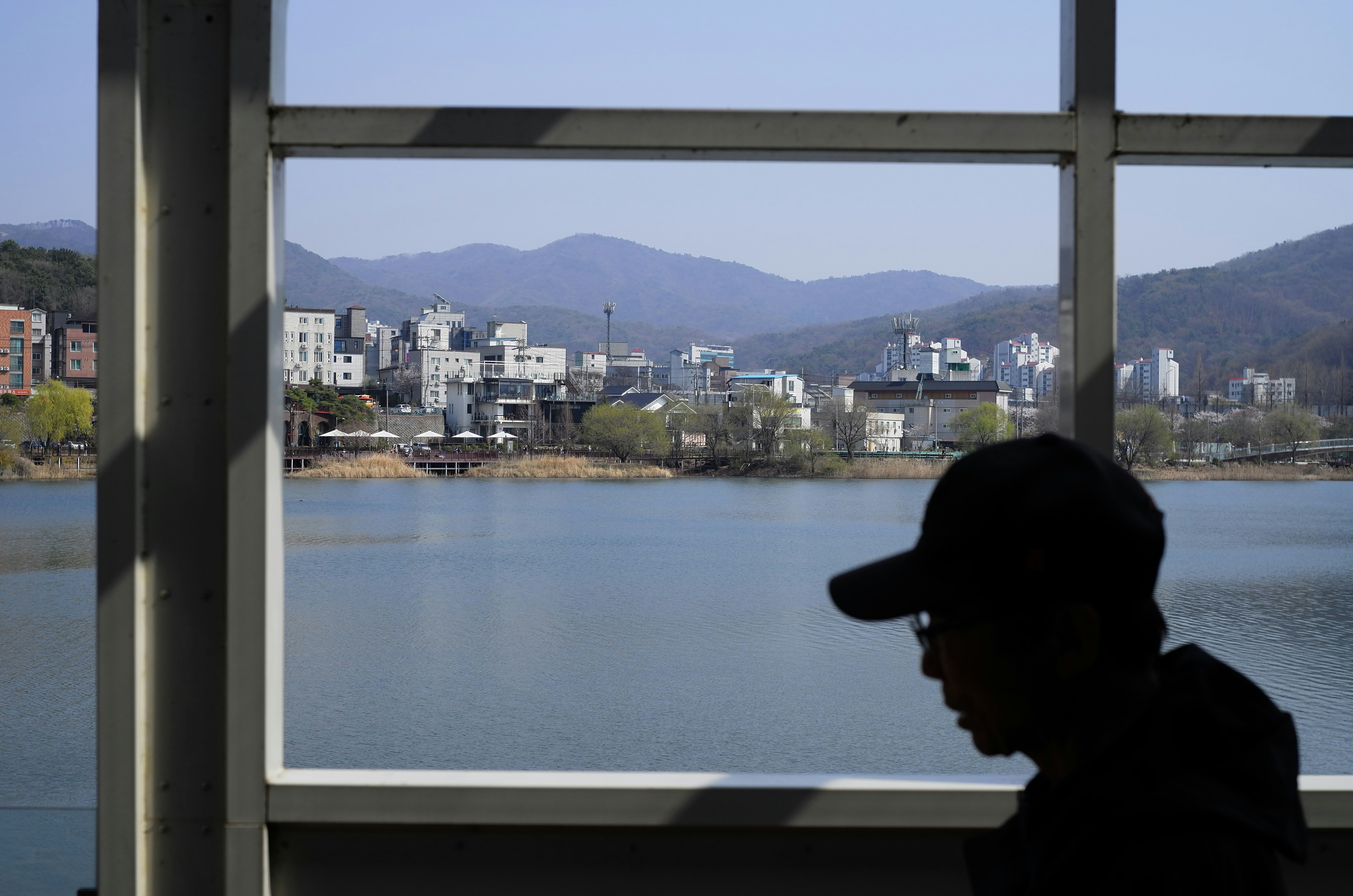 Silhouette by the Window: City Across the Quiet Lake