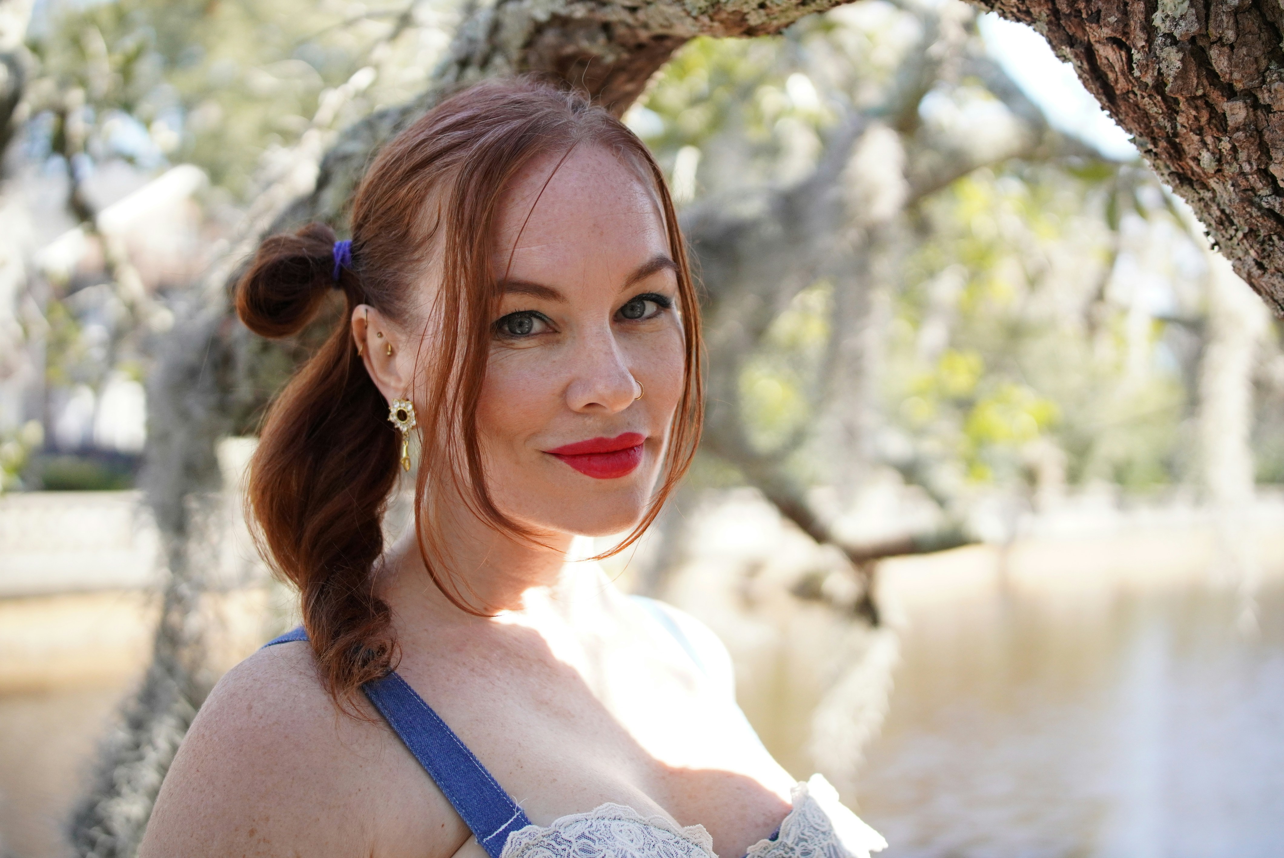 Portrait under a sunlit tree: bold red lips and soft azure dress