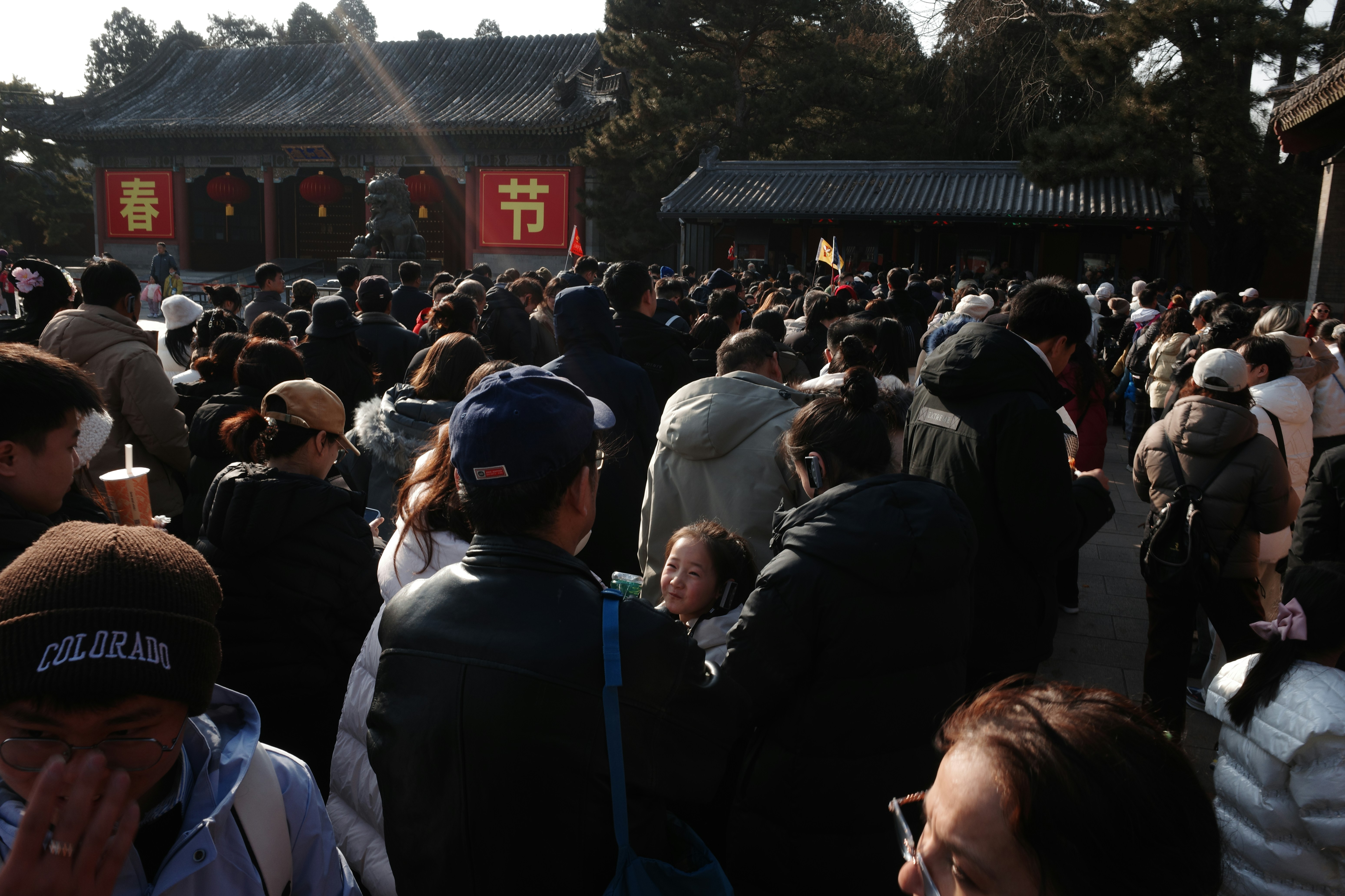 Crowd at a temple festival with red banners and stone statue backdrop