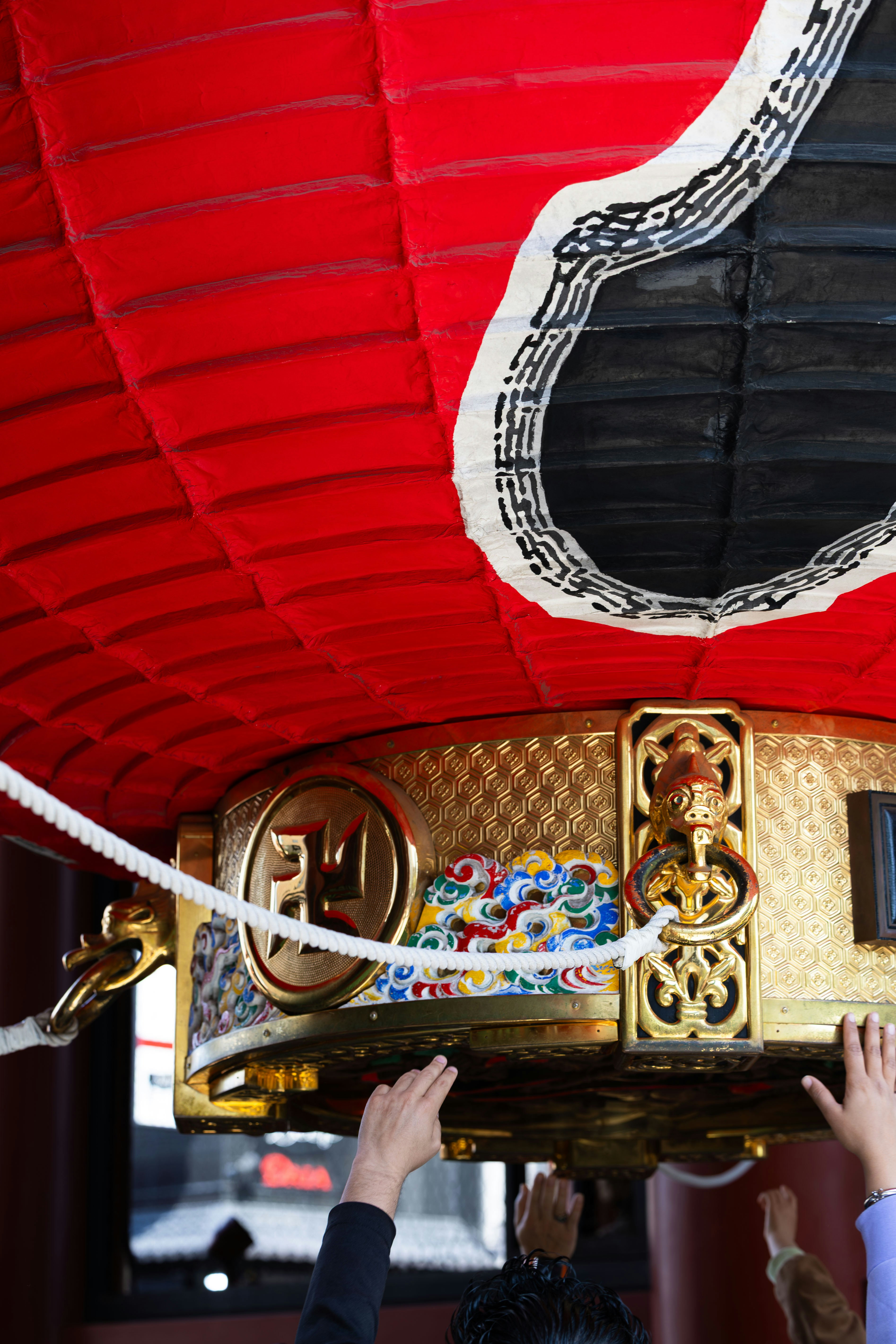 Orb of tradition: Hands lift a gilded temple lantern under a crimson canopy