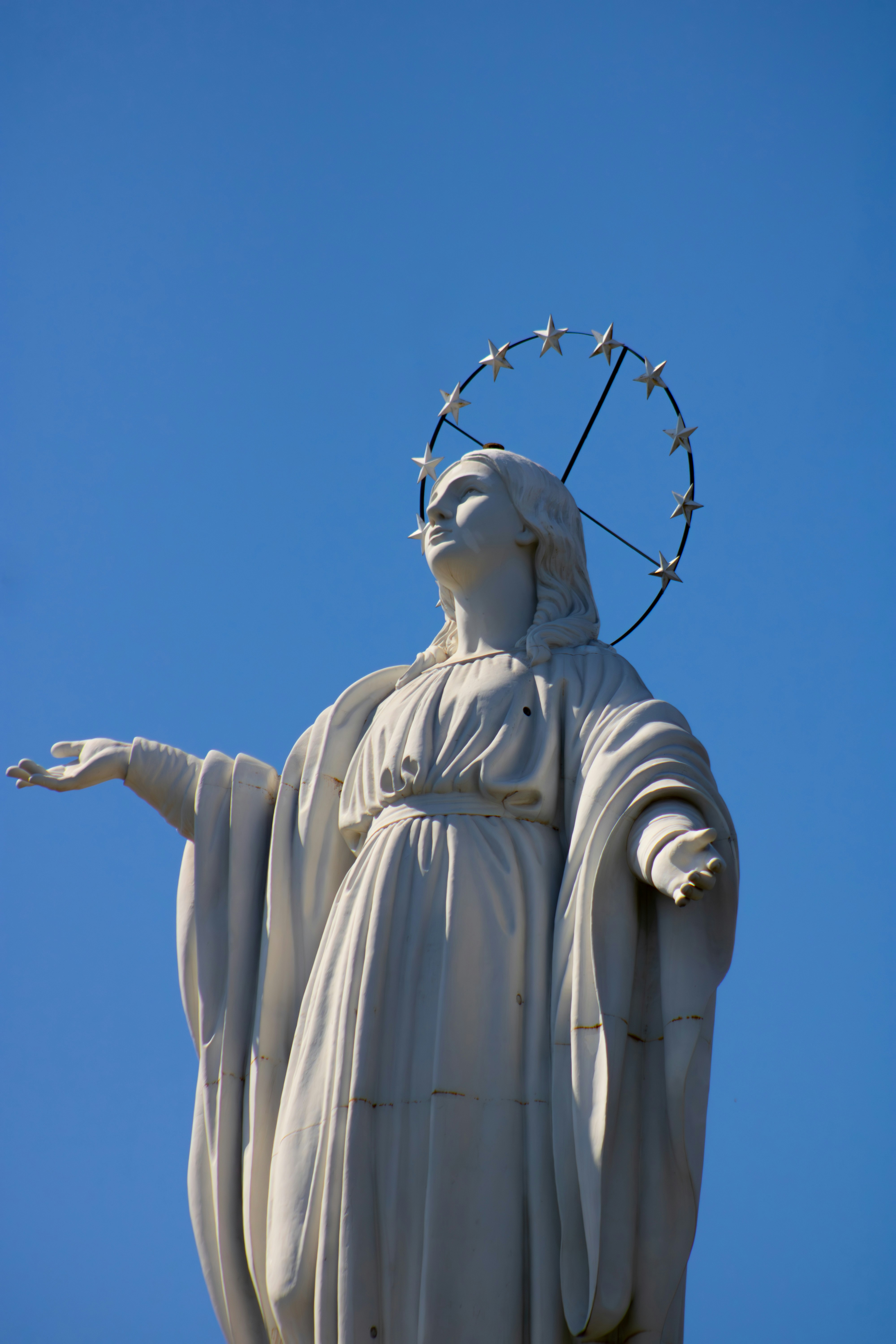 Ascendant Grace: The Virgin Statue Beneath a Clear Blue Sky