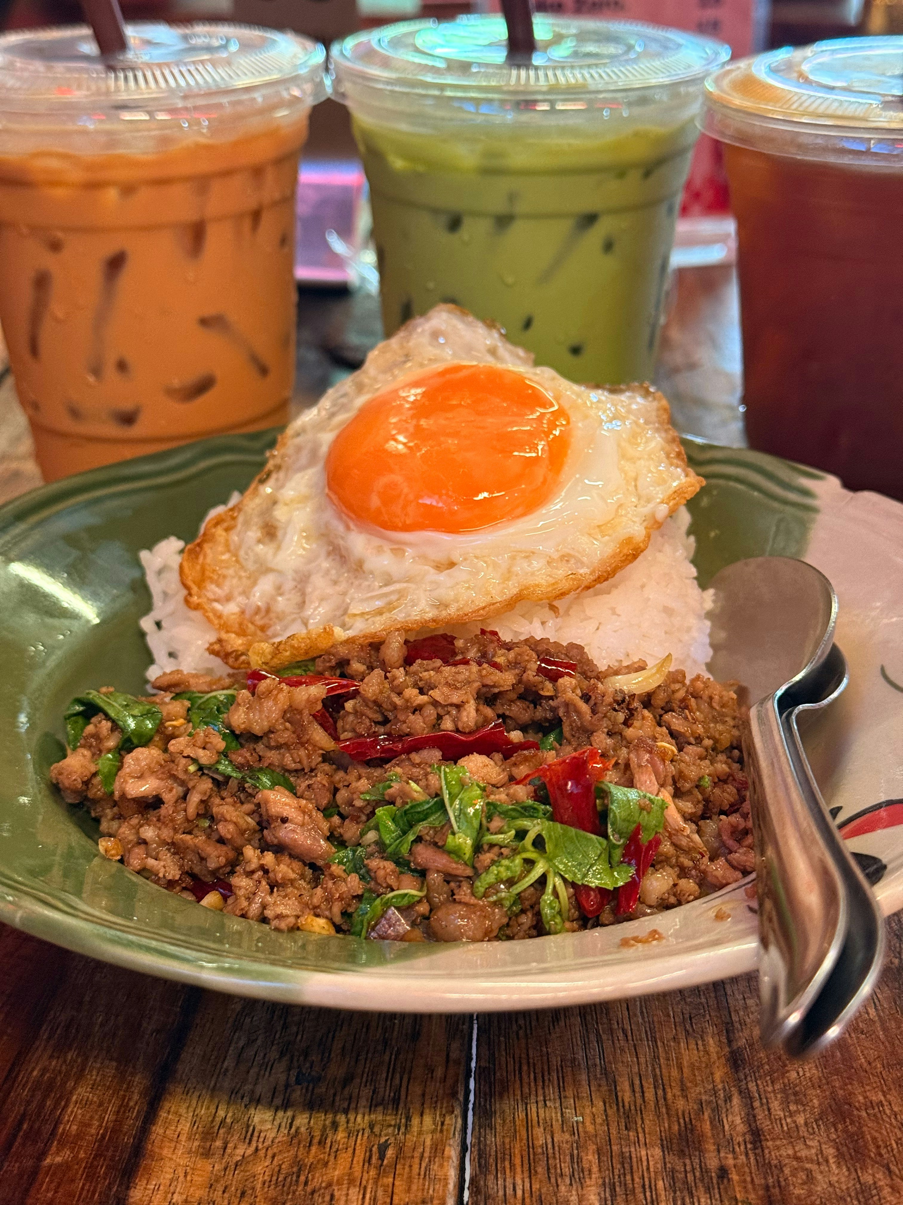 Thai-style minced pork with fried egg over rice, framed by iced beverages