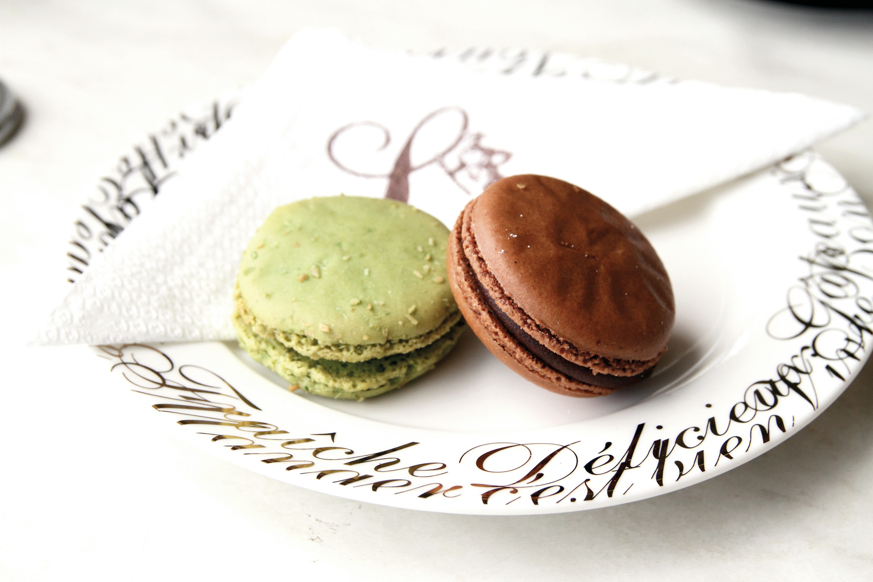Two macarons resting on a decorative plate with script