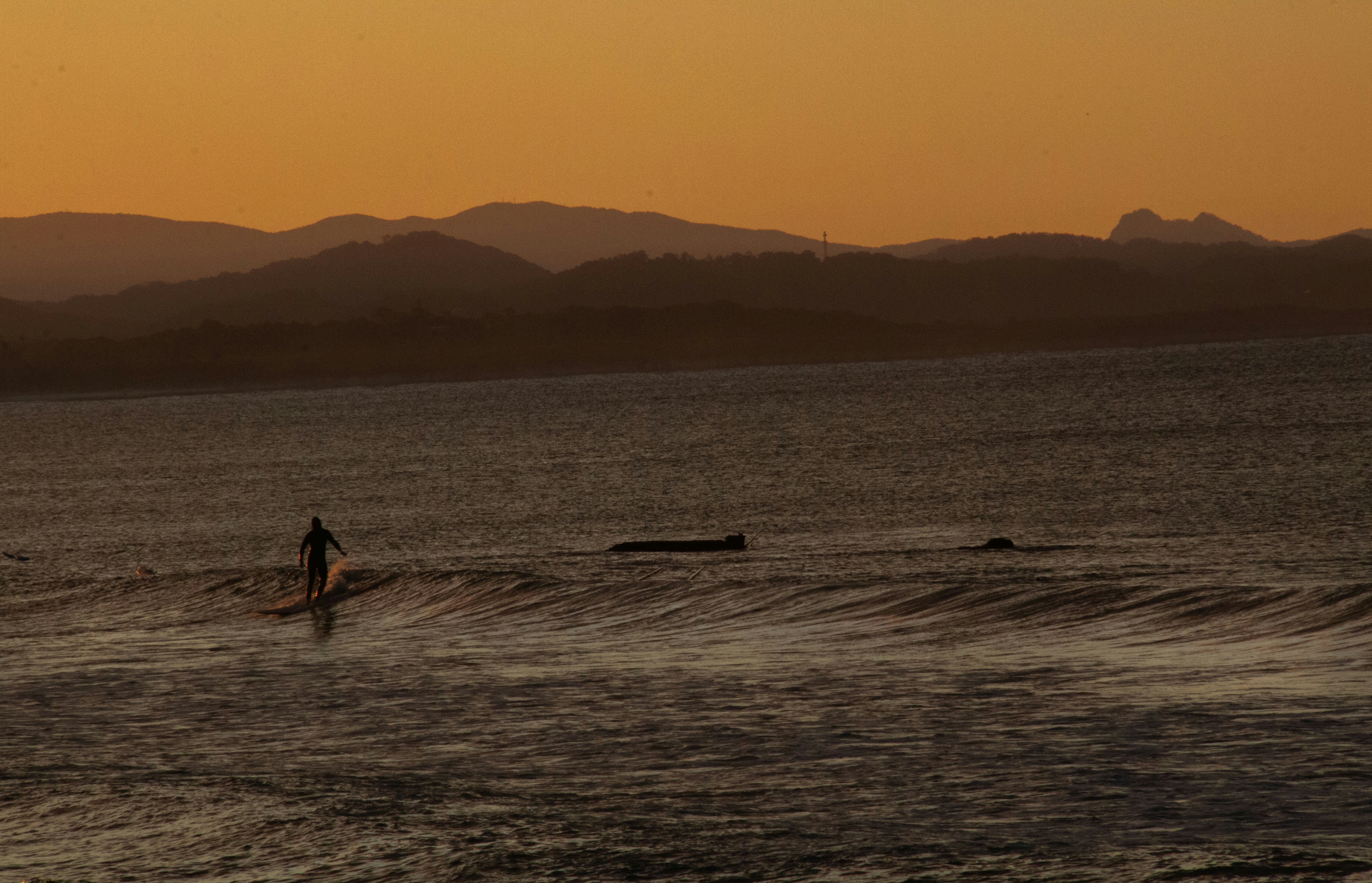 Silhouette at Sunset: Surfer and Ripples against a Distant Ridge