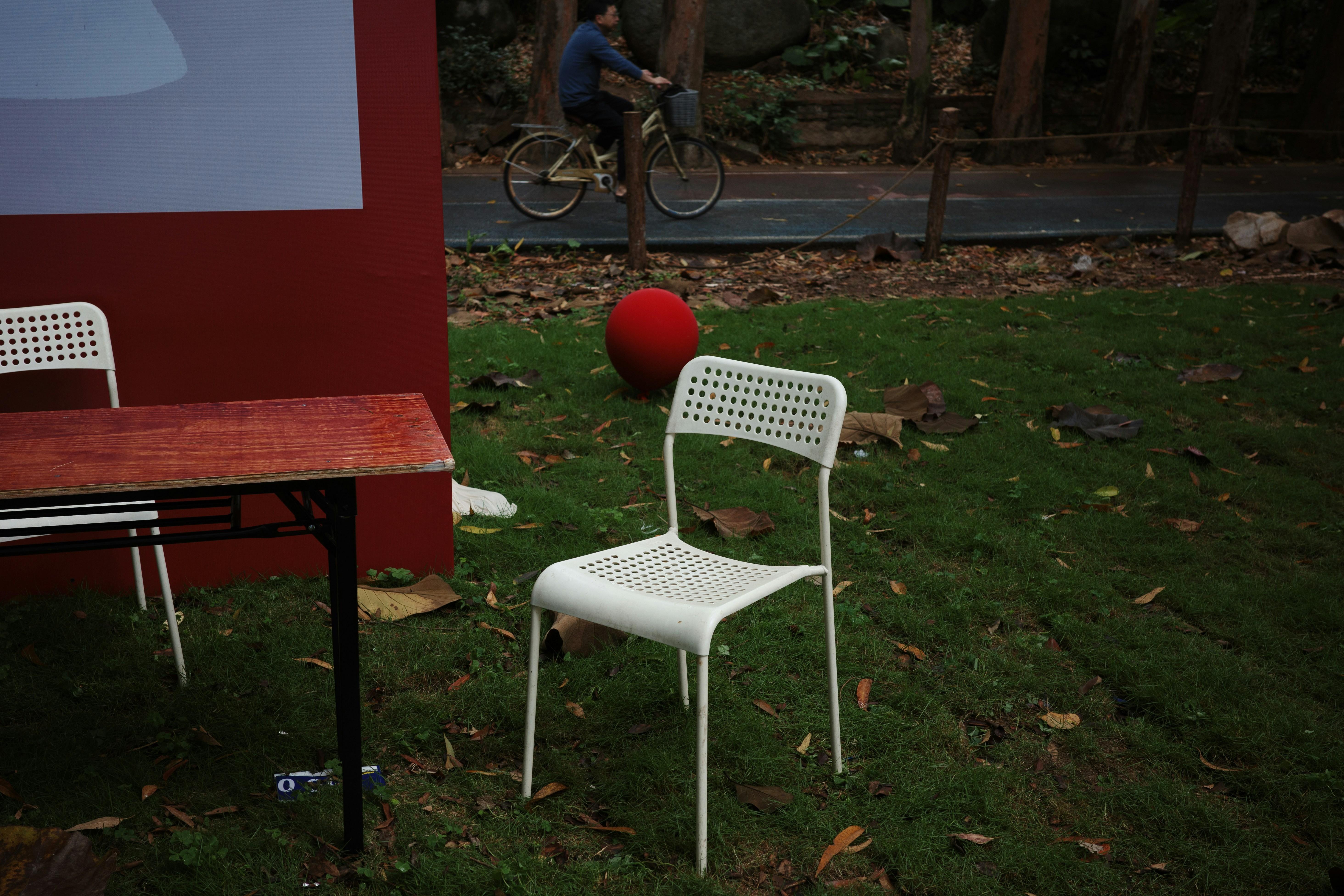 White perforated chair under a red shelter with scattered leaves