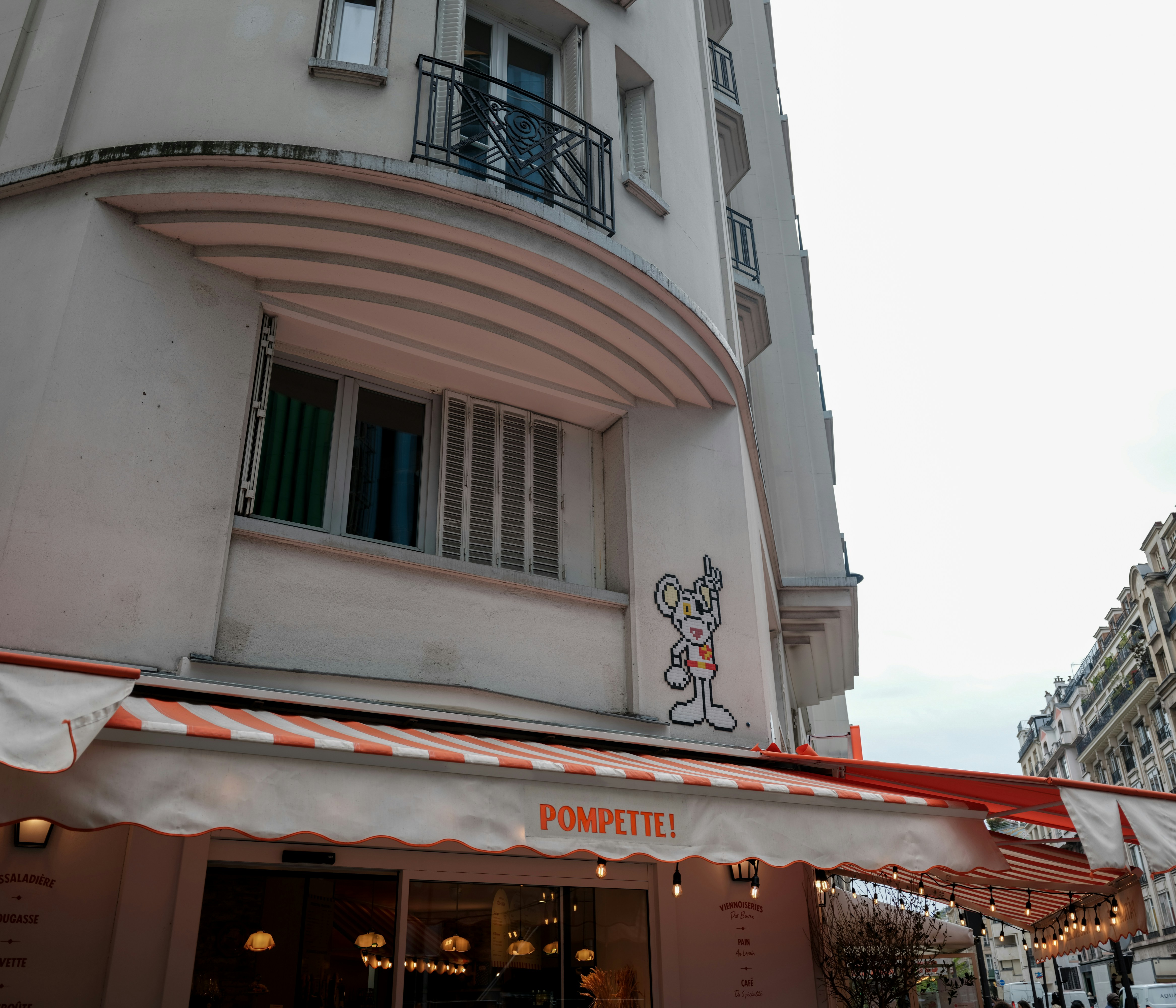 Curve of the Corner Café: A Cartoon Mascot Salutes from the Balcony