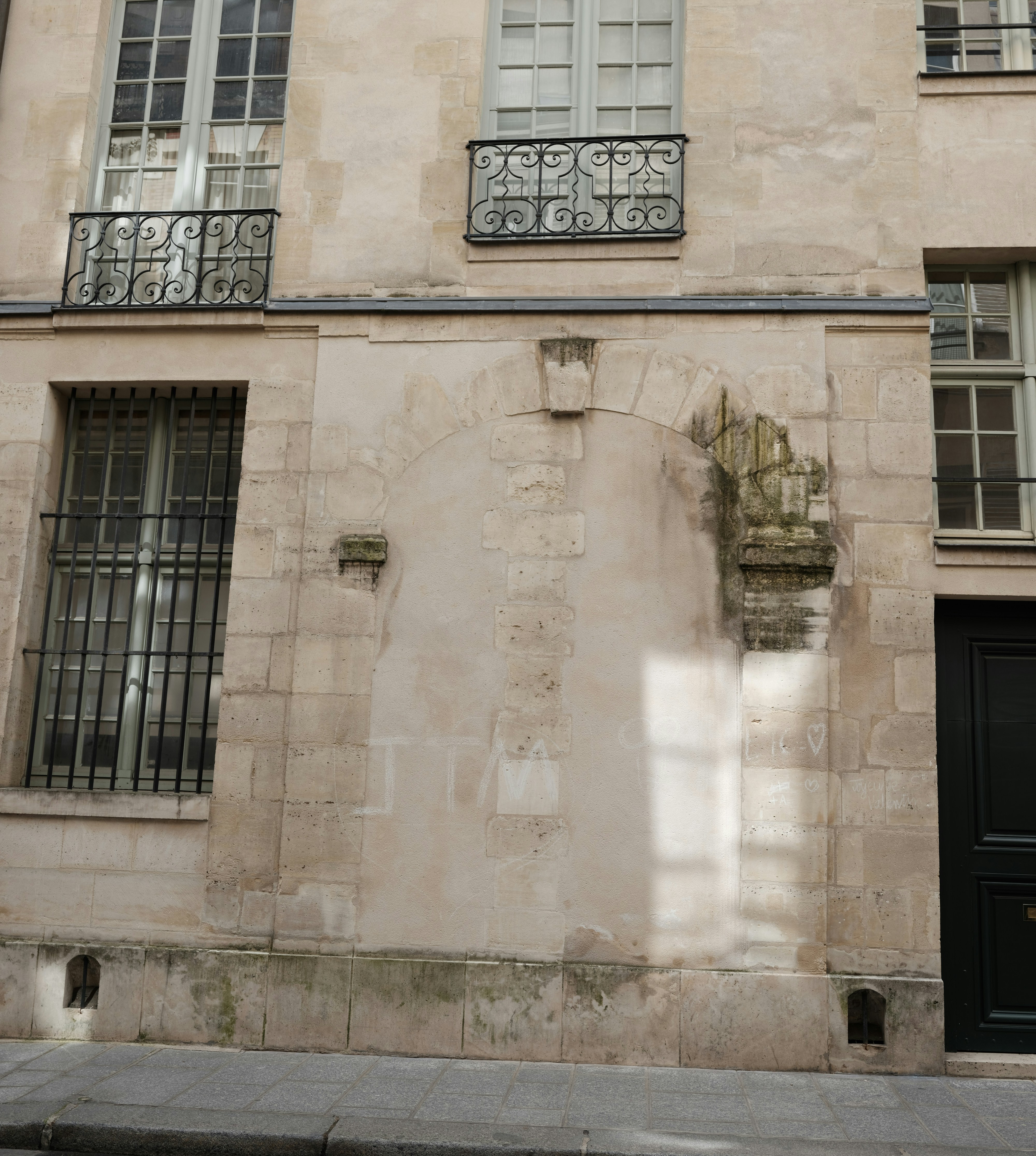 Faded Facade with Shadowed Archway and Iron Balcony
