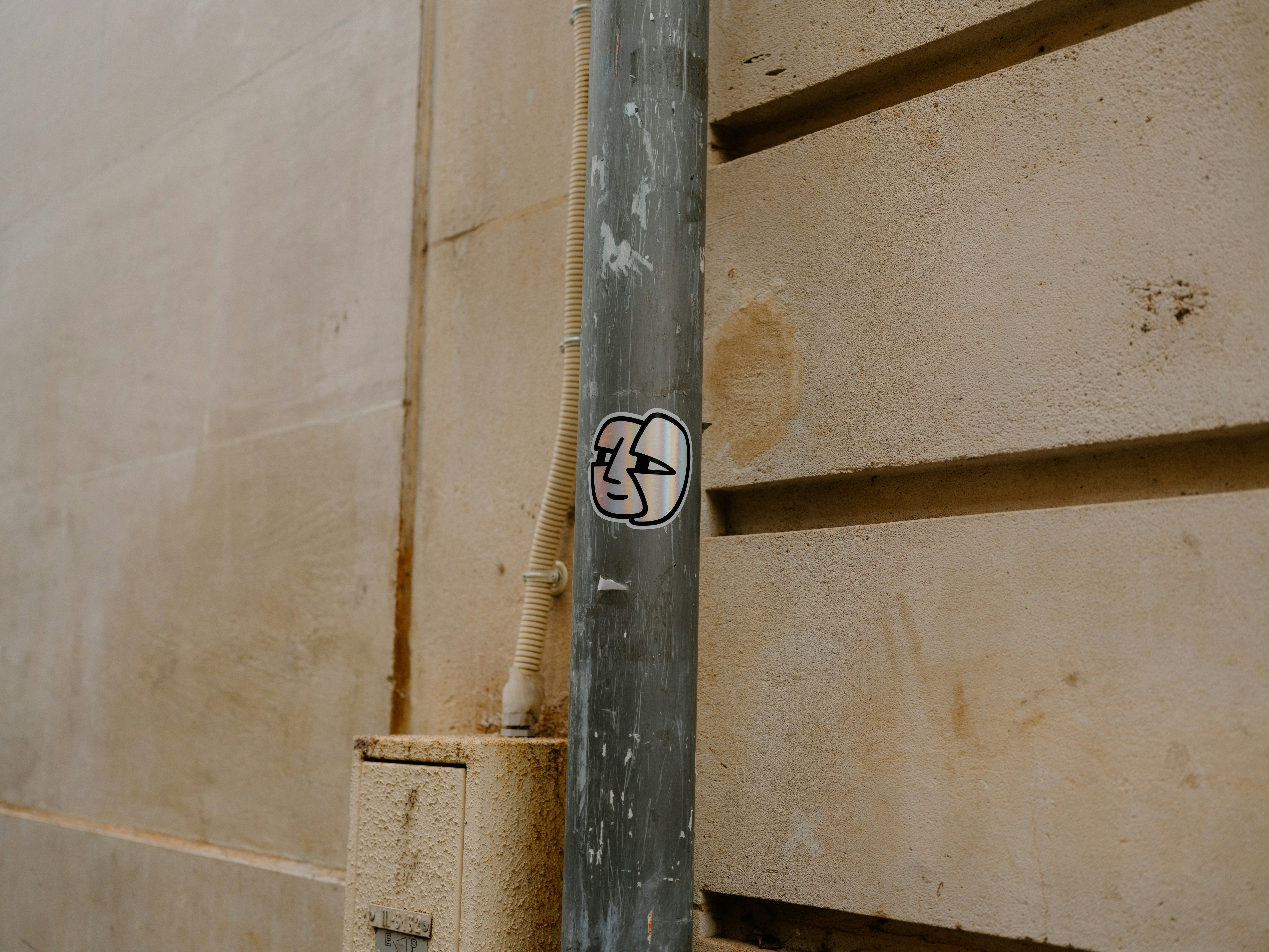 Stickered Utility Pole Framed by Exterior Wall