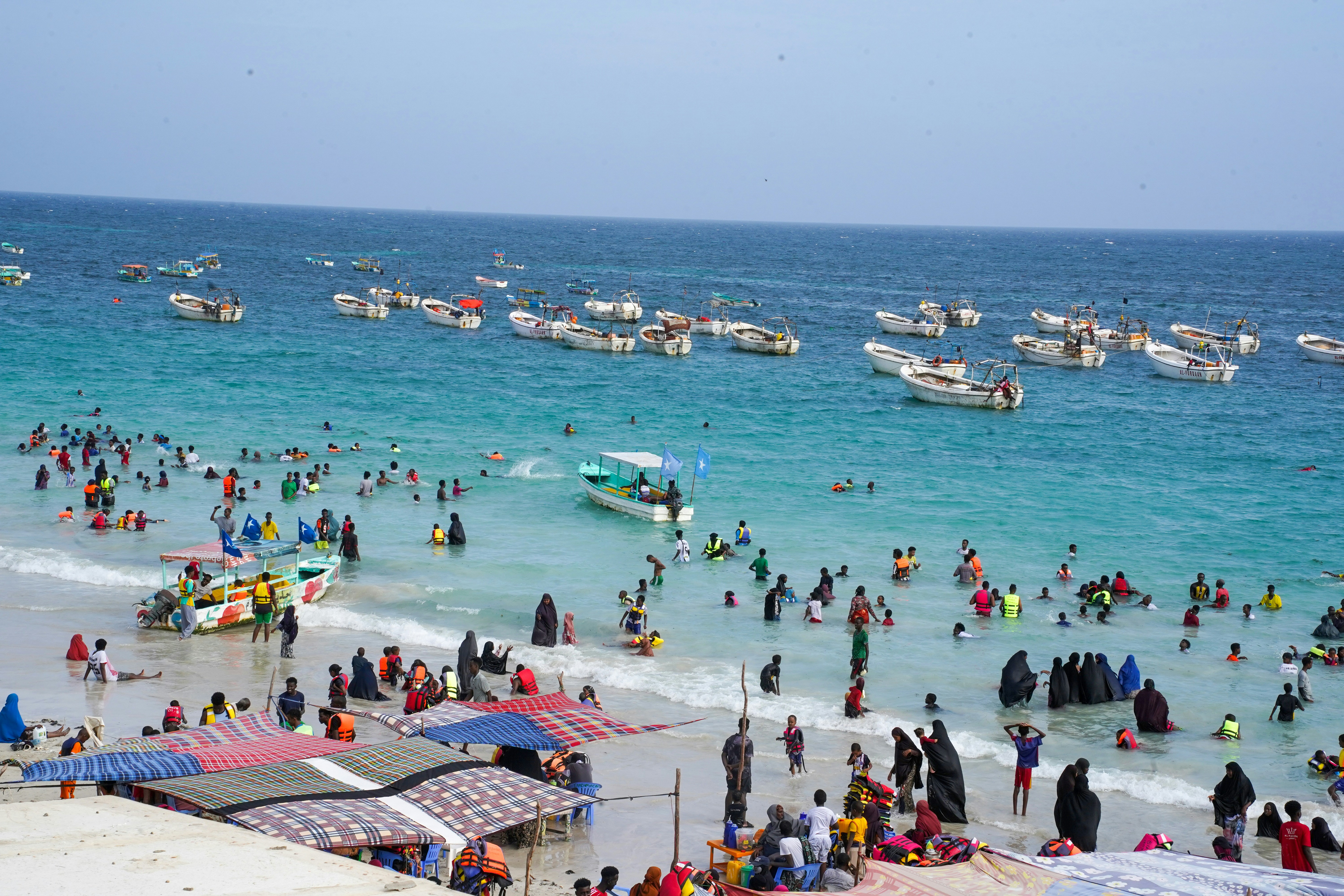 Sunlit Coastline: A Sea of Swimwear and Boats along a Bustling Beach