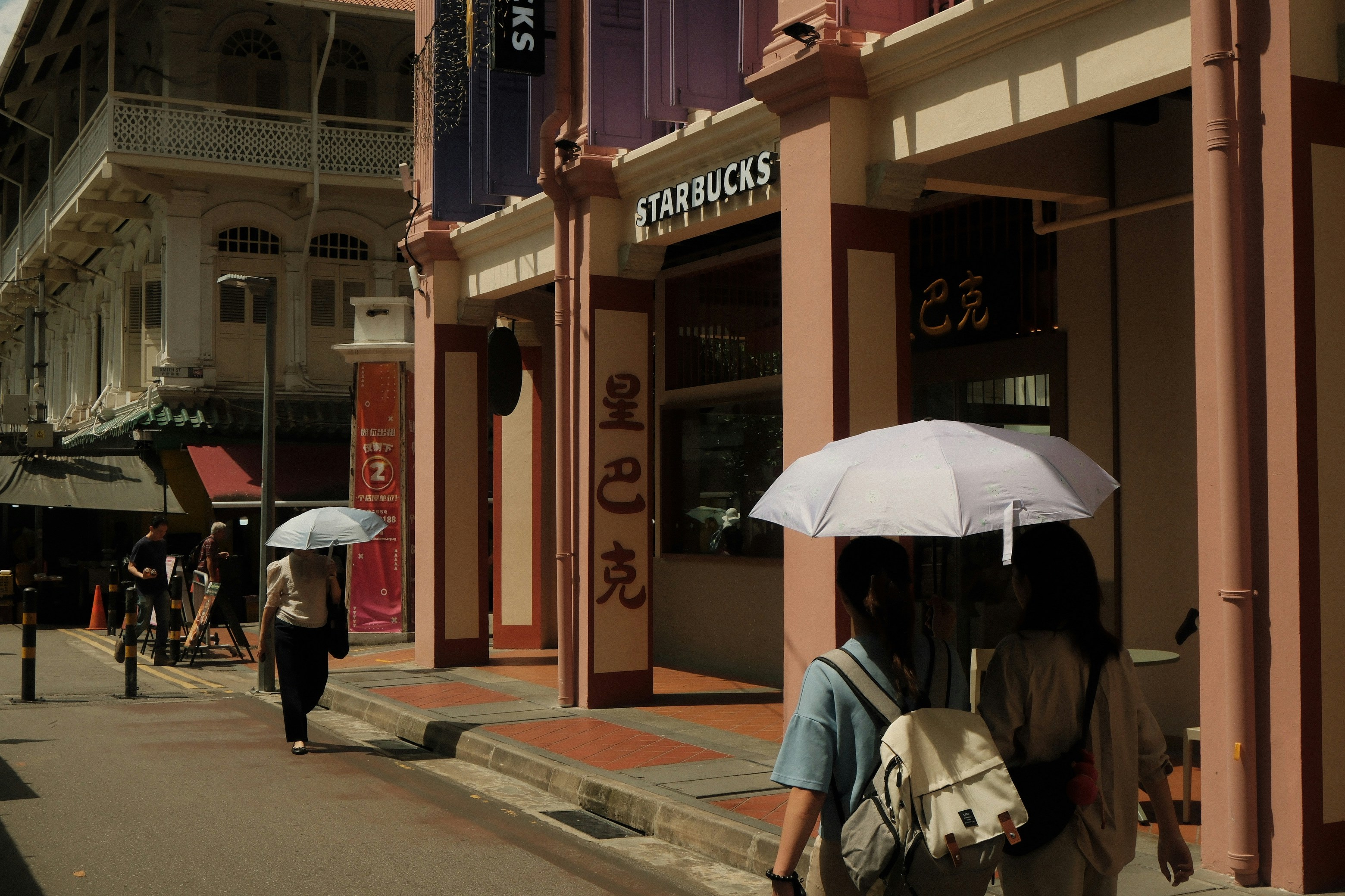 People walk with umbrellas on a sunny street.