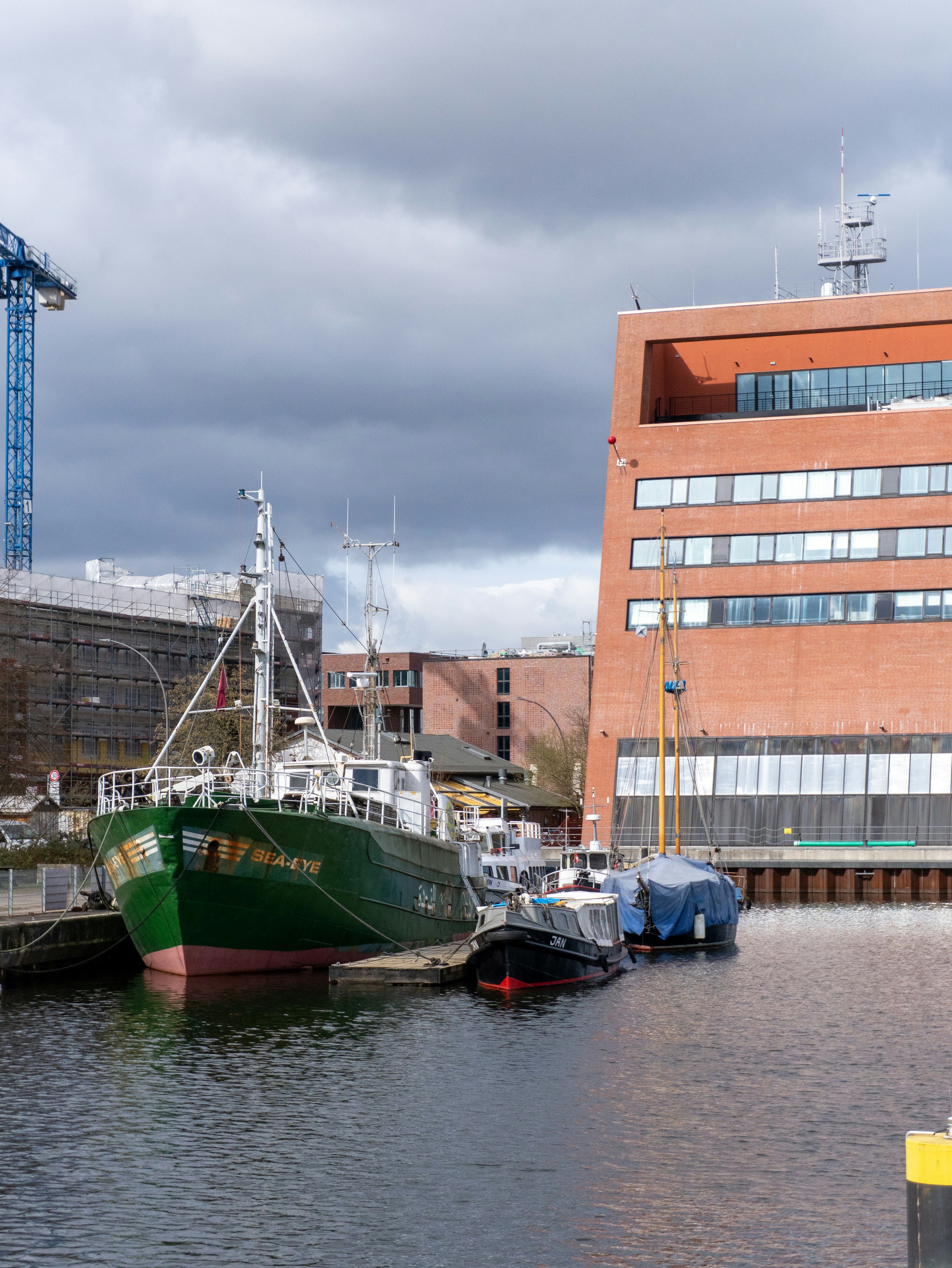 Harbor Sentinel: A Green Gaffler in Front of Modern Brick