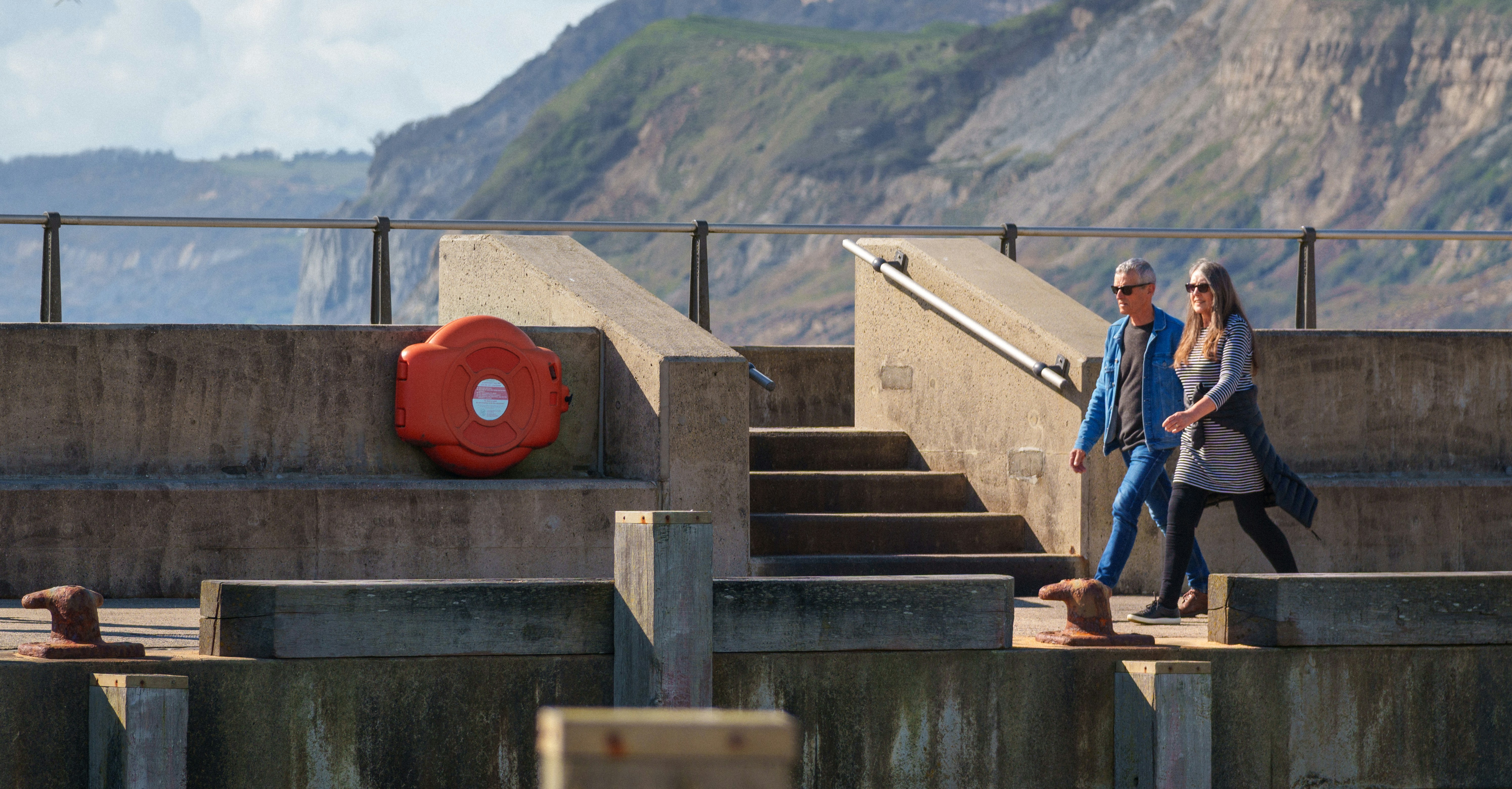 Staged stride along the harbor stairs: a couple in motion against distant cliffs