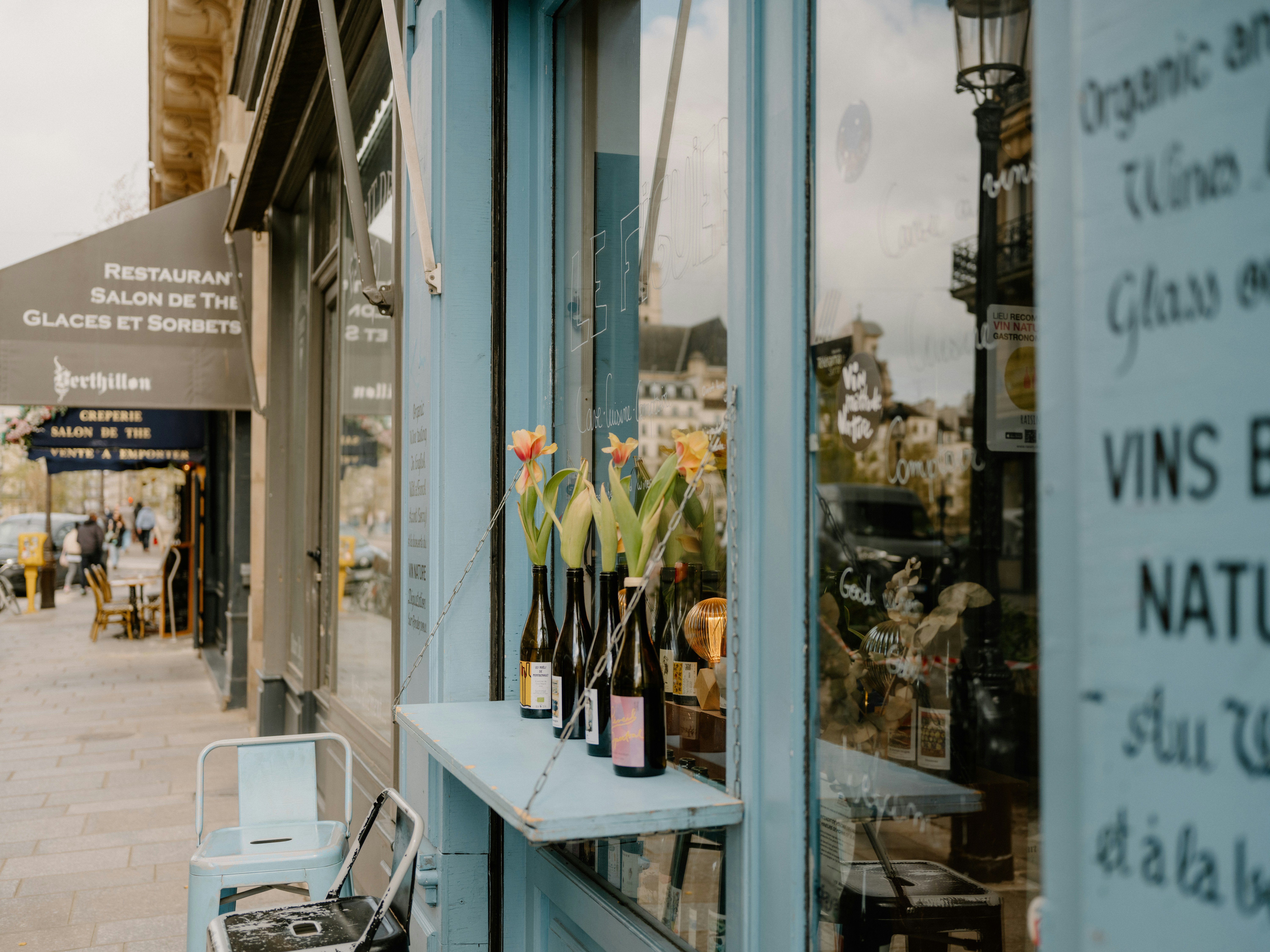 Blue storefronts and tulips: a quiet street vignette with wine bottles on a window ledge
