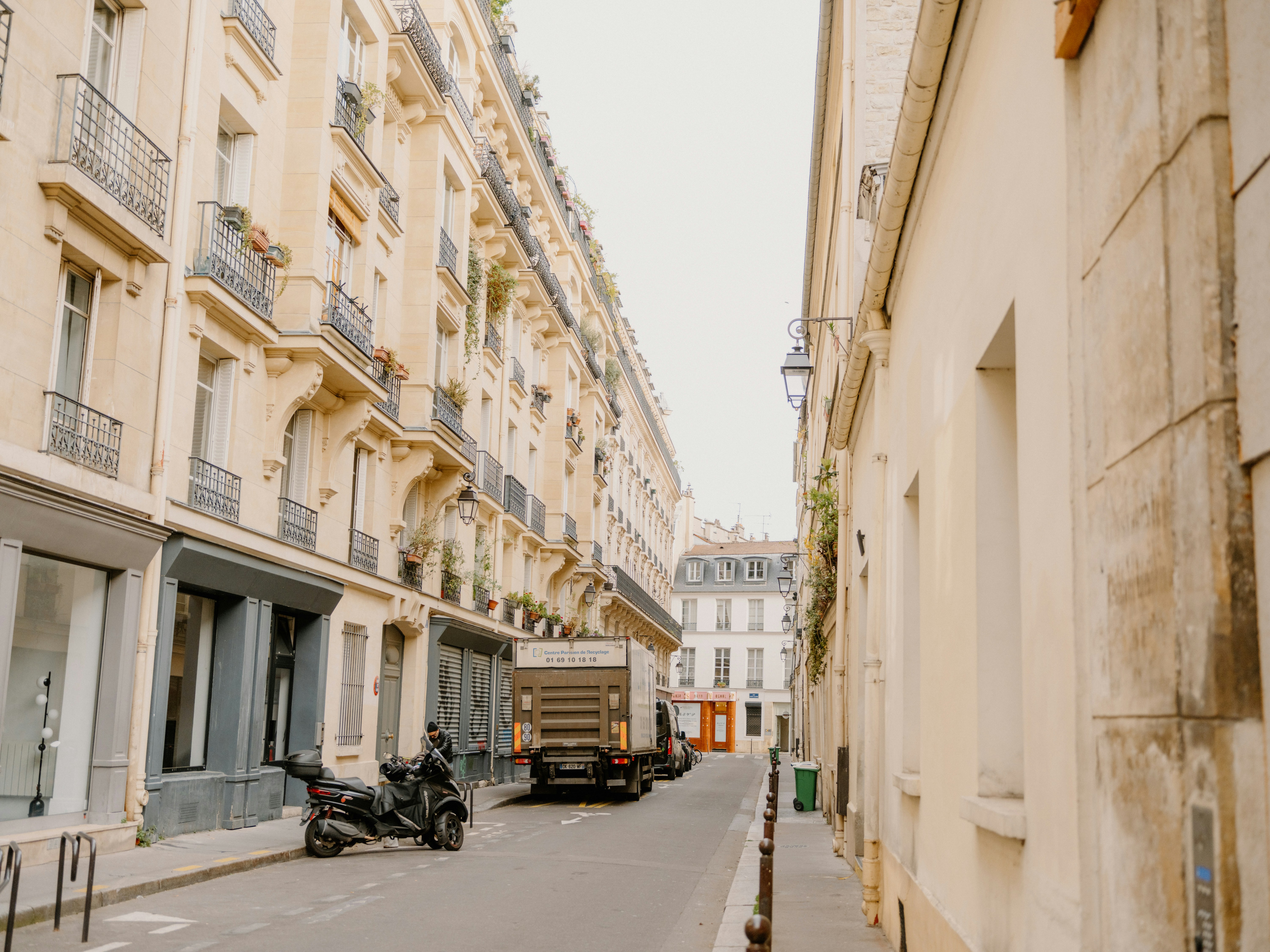 A narrow street in paris with buildings and parked vehicles.