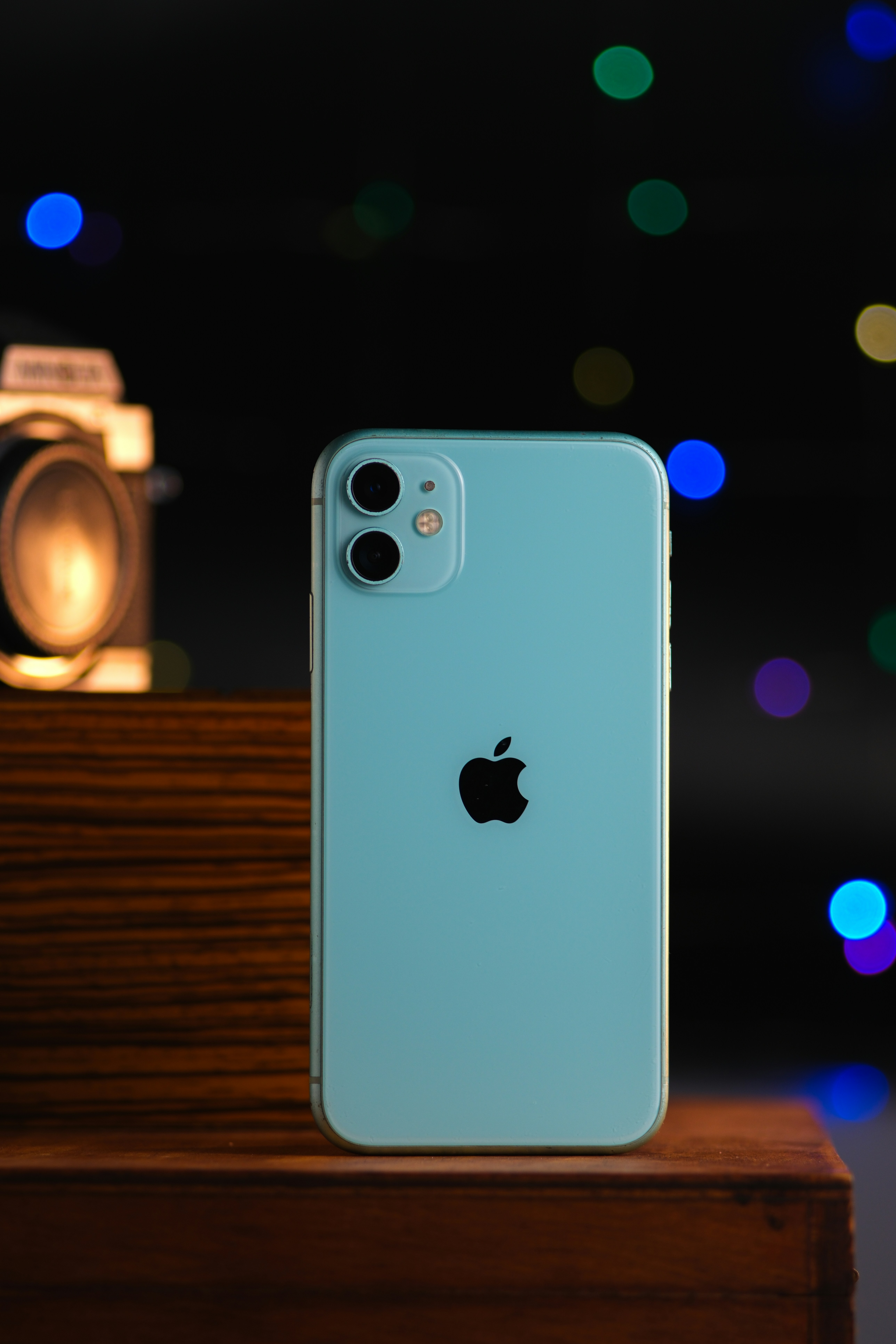 Aqua-glass iPhone on a wooden pedestal under ambient city glow