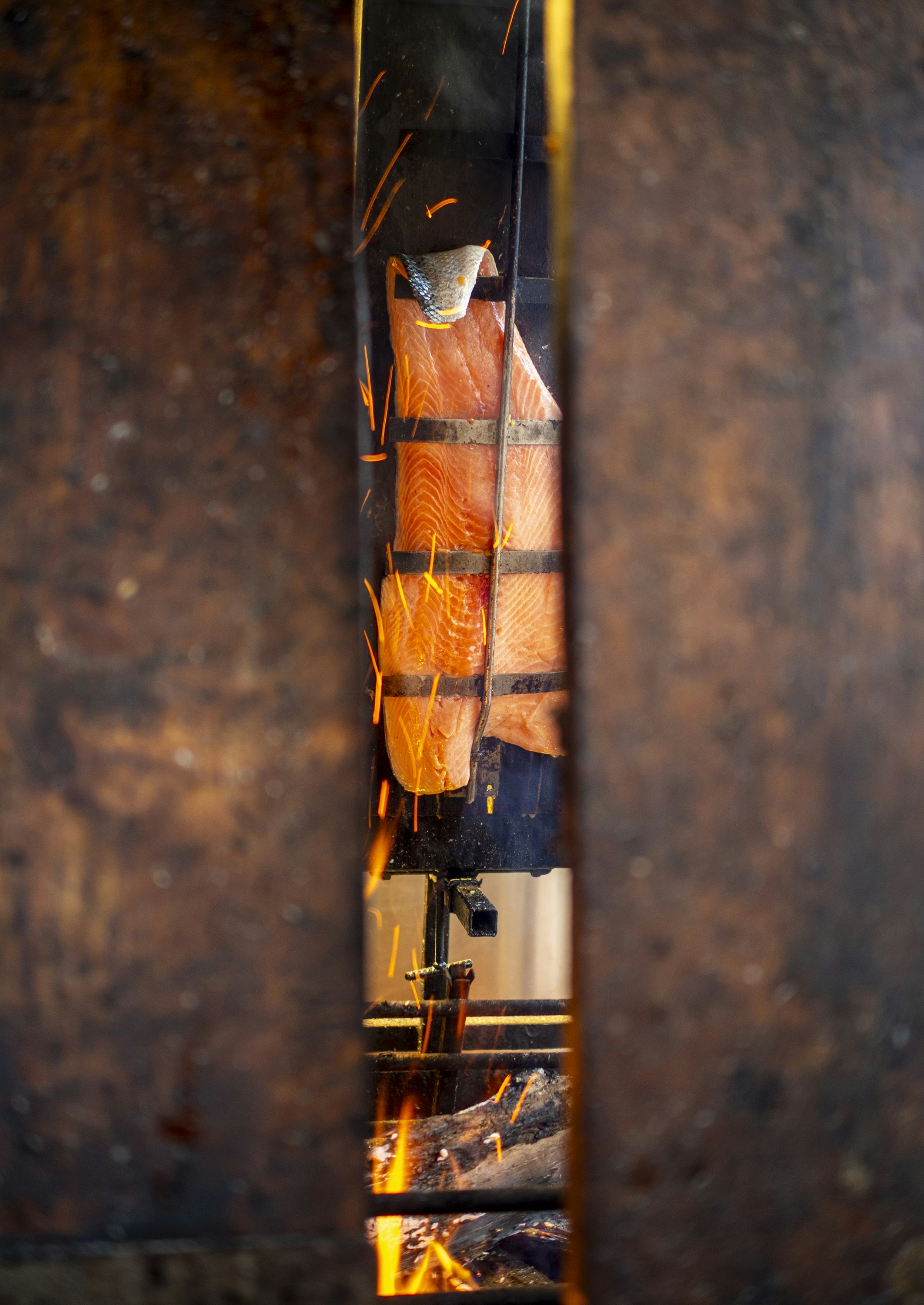 A narrow vertical slice reveals glowing orange sparks and metal shavings inside a sawmill or forge, framed by dark wooden surroundings.
