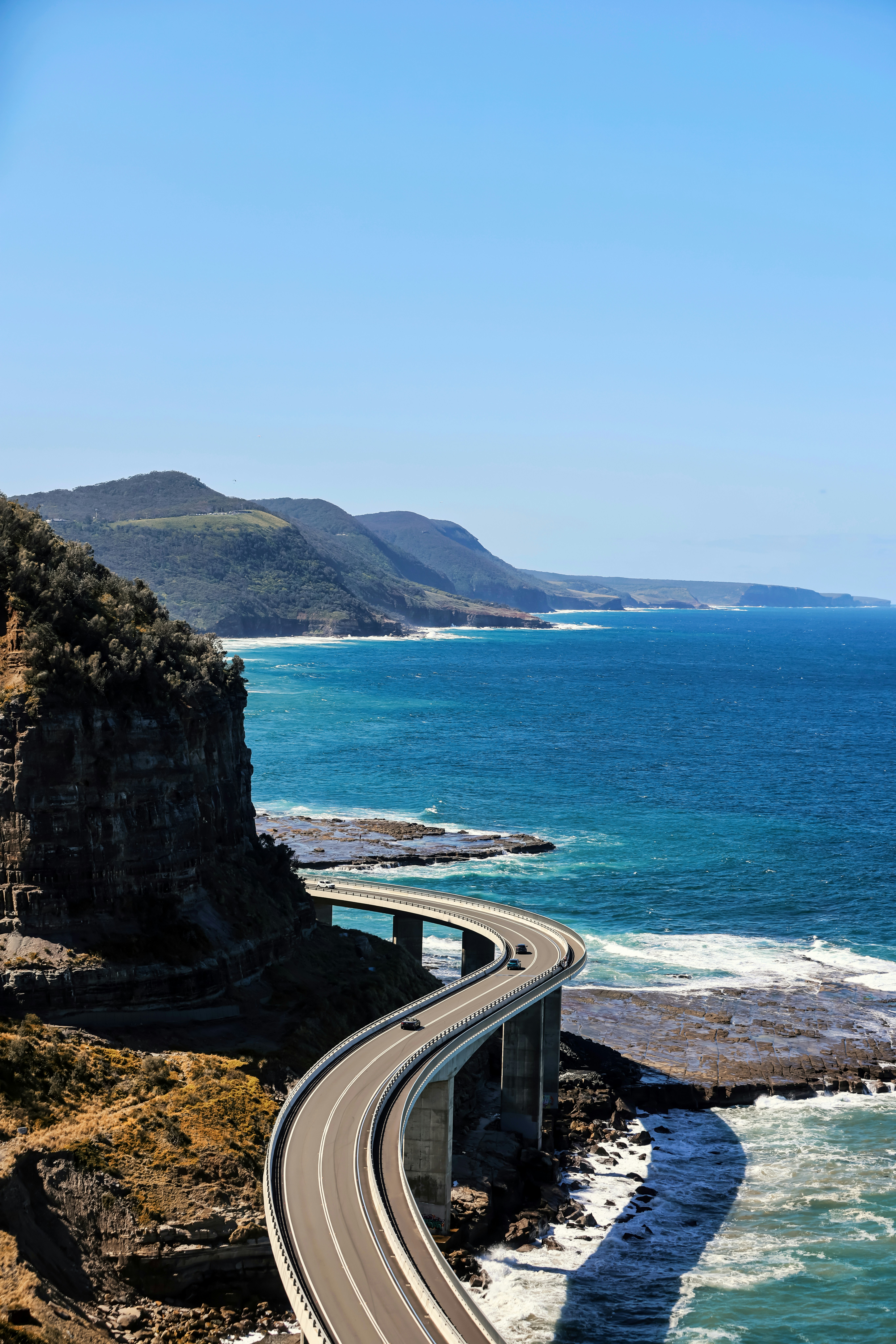 Coastal Curve: A winding bridge stepping along the cliffside into a blue horizon