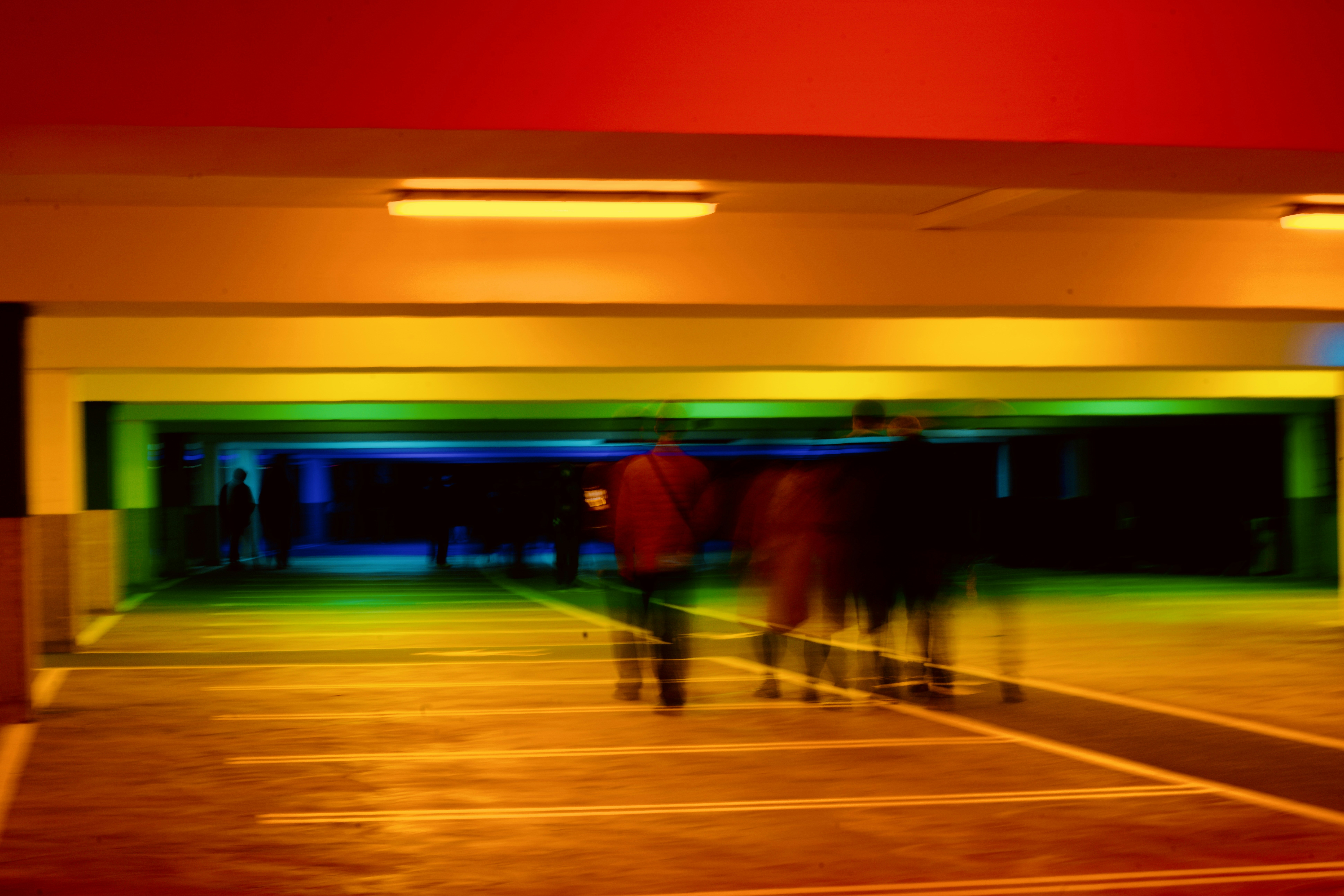Neon Corridor: A Blur of Figures Beneath Colored Overpasses