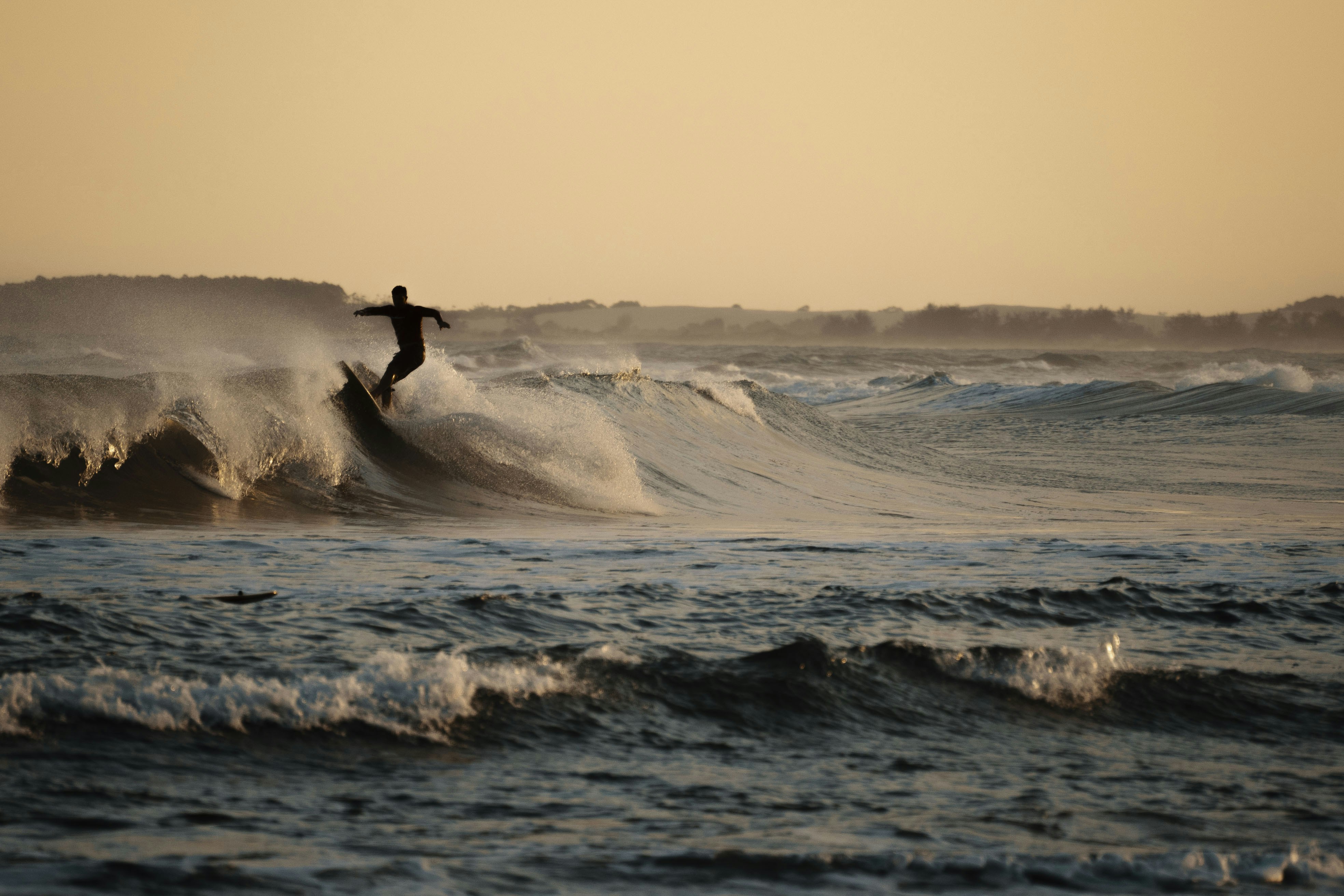 Surf silhouette against a warm horizon: a lone rider carving a golden crest