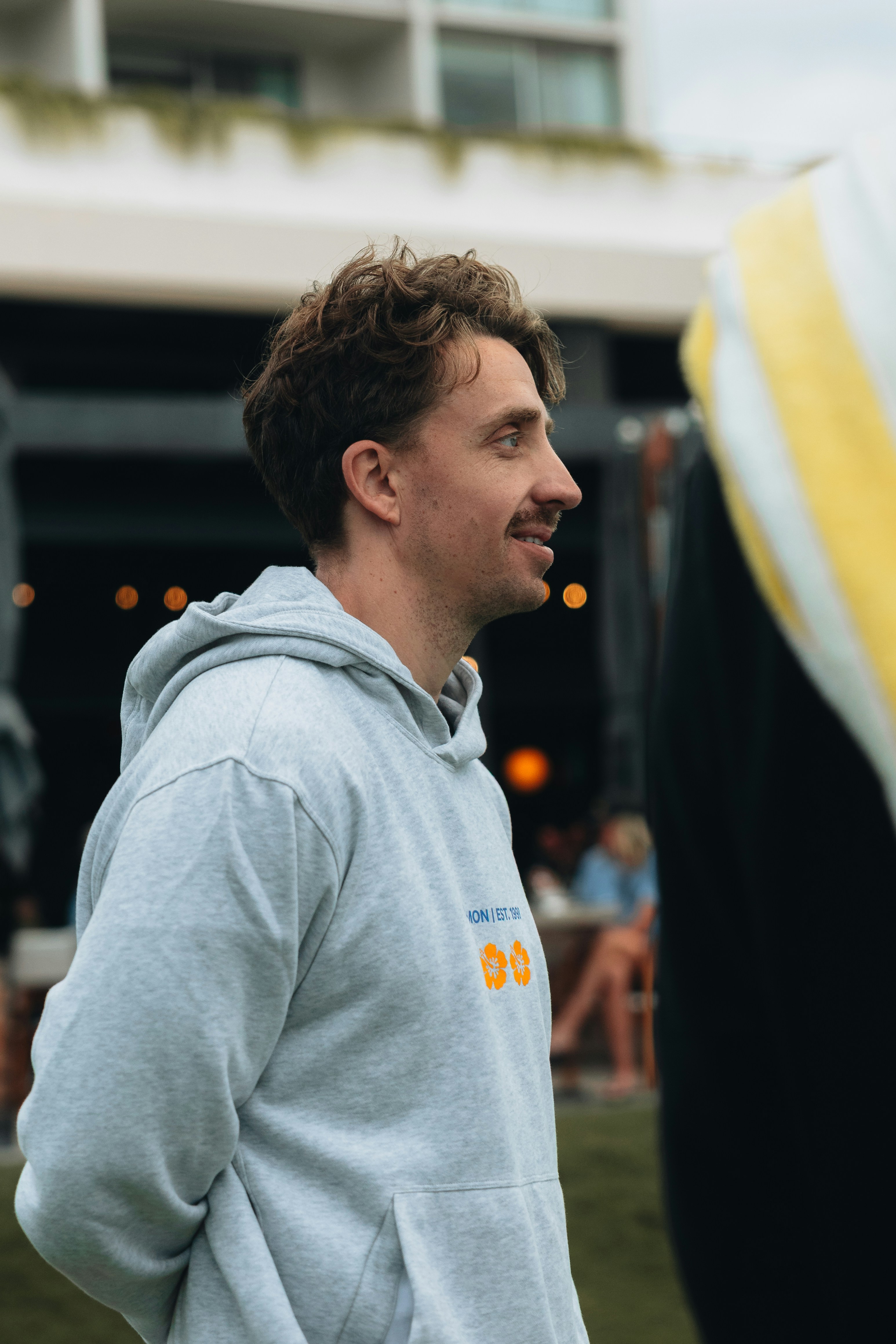 Side-profile of a man in a light hoodie at an outdoor event