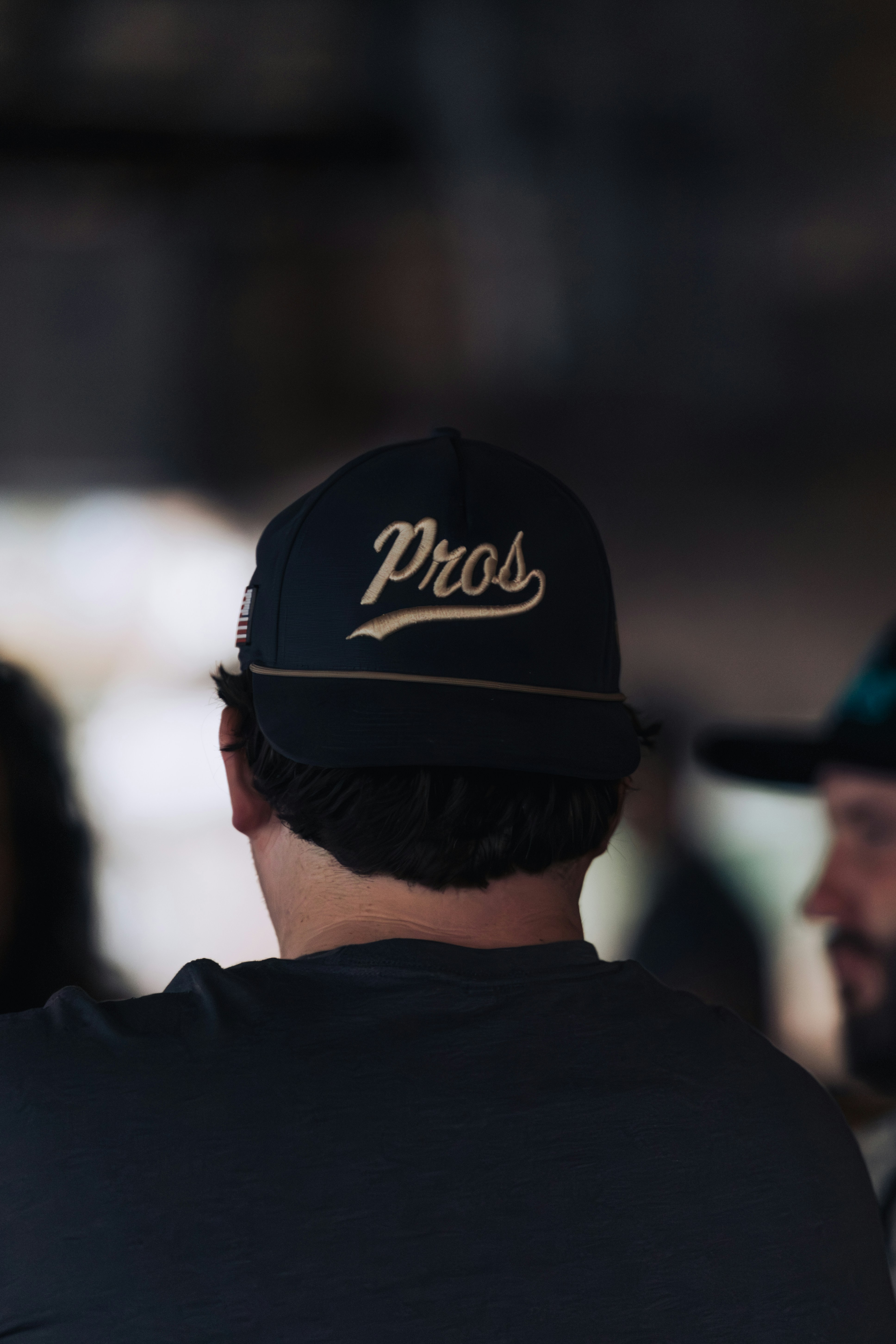 Back of a man’s cap reading 'Pros' in a softly blurred setting