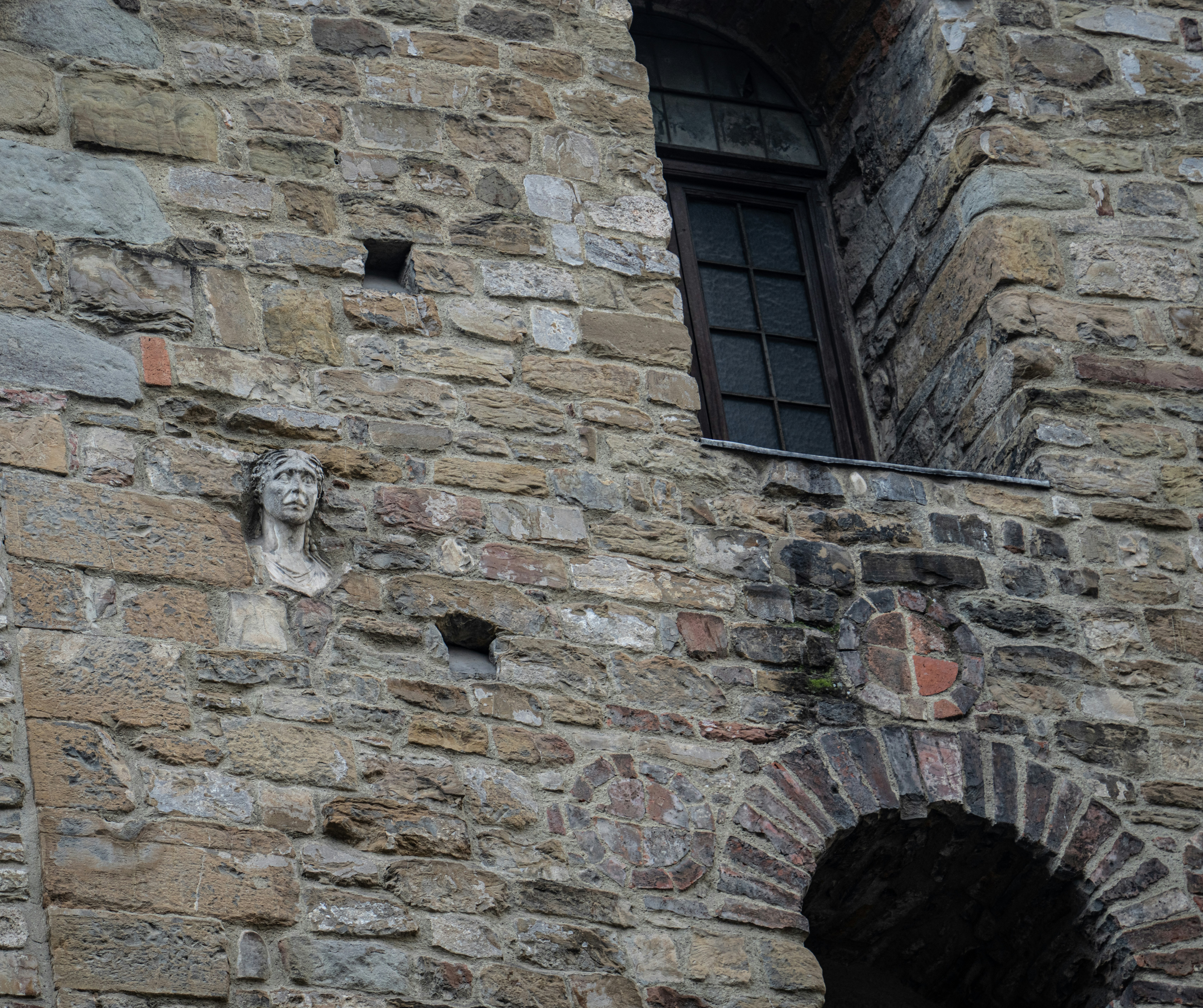 Stone wall with carved bust overlooking a dark arch