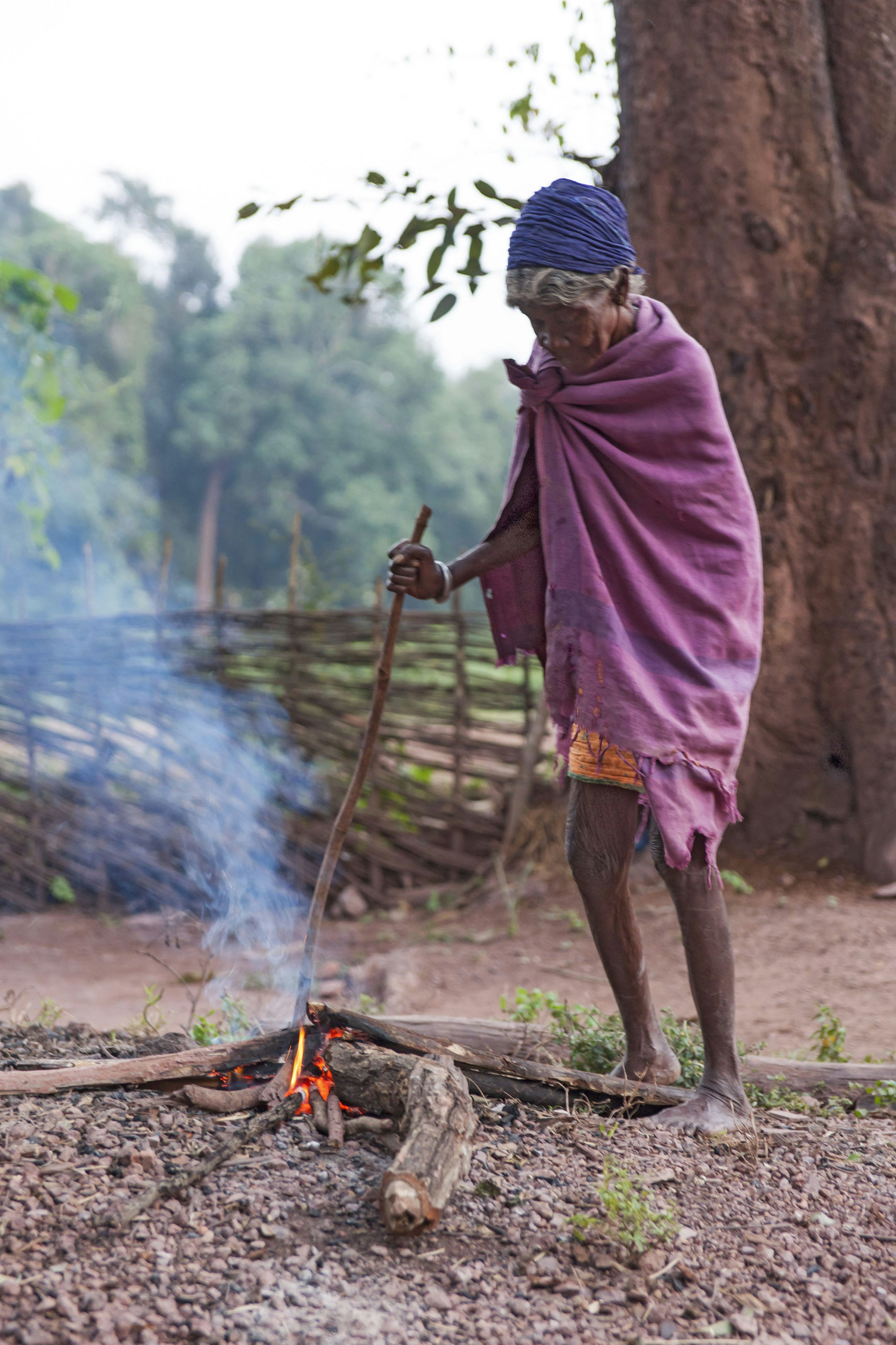 The Ember Keeper: An Elderly Figure tending a fire in a Rural Clearing