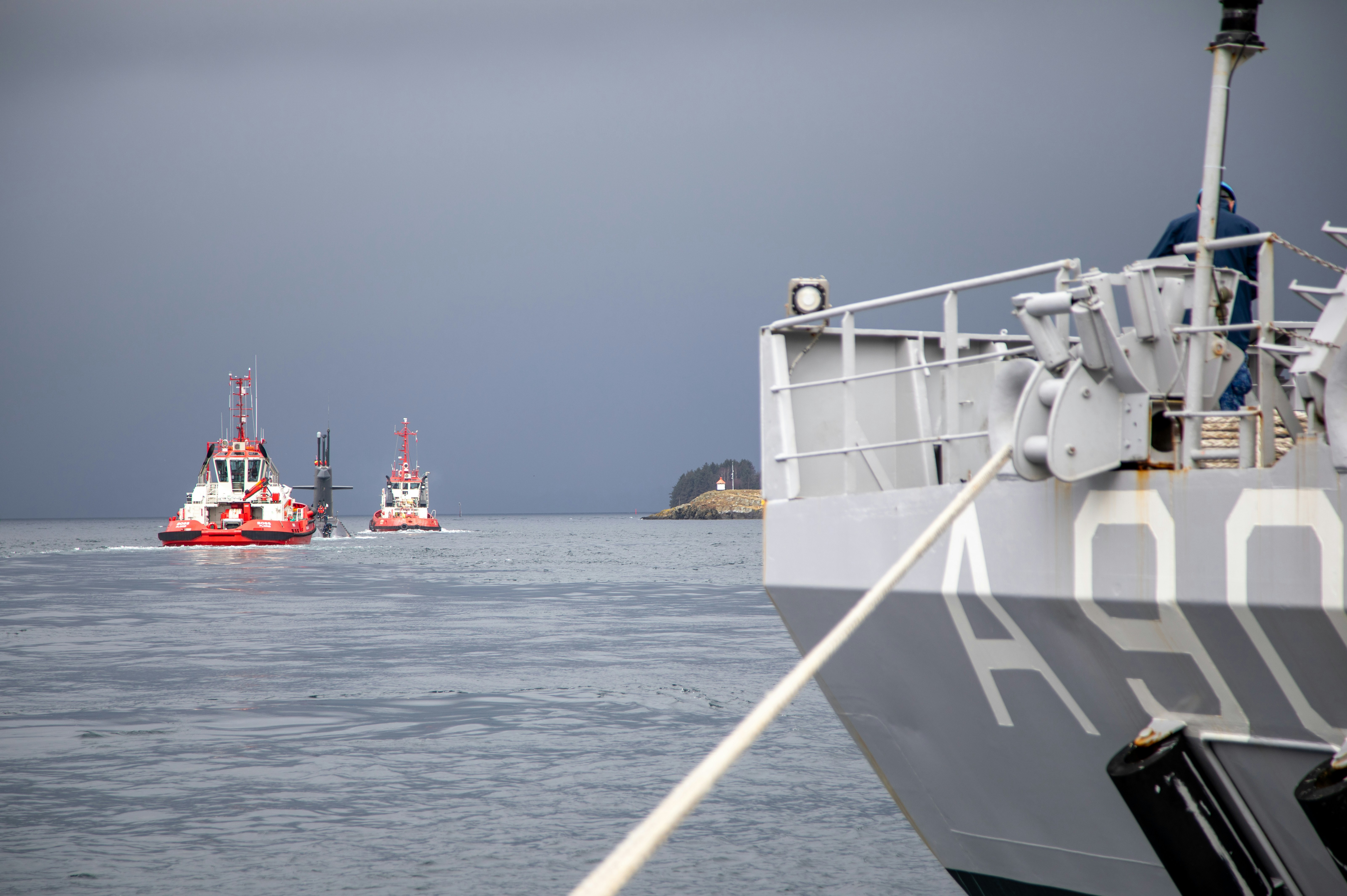 Two red tugboats on calm sea approach a distant buoy, flanked by a looming freighter hull