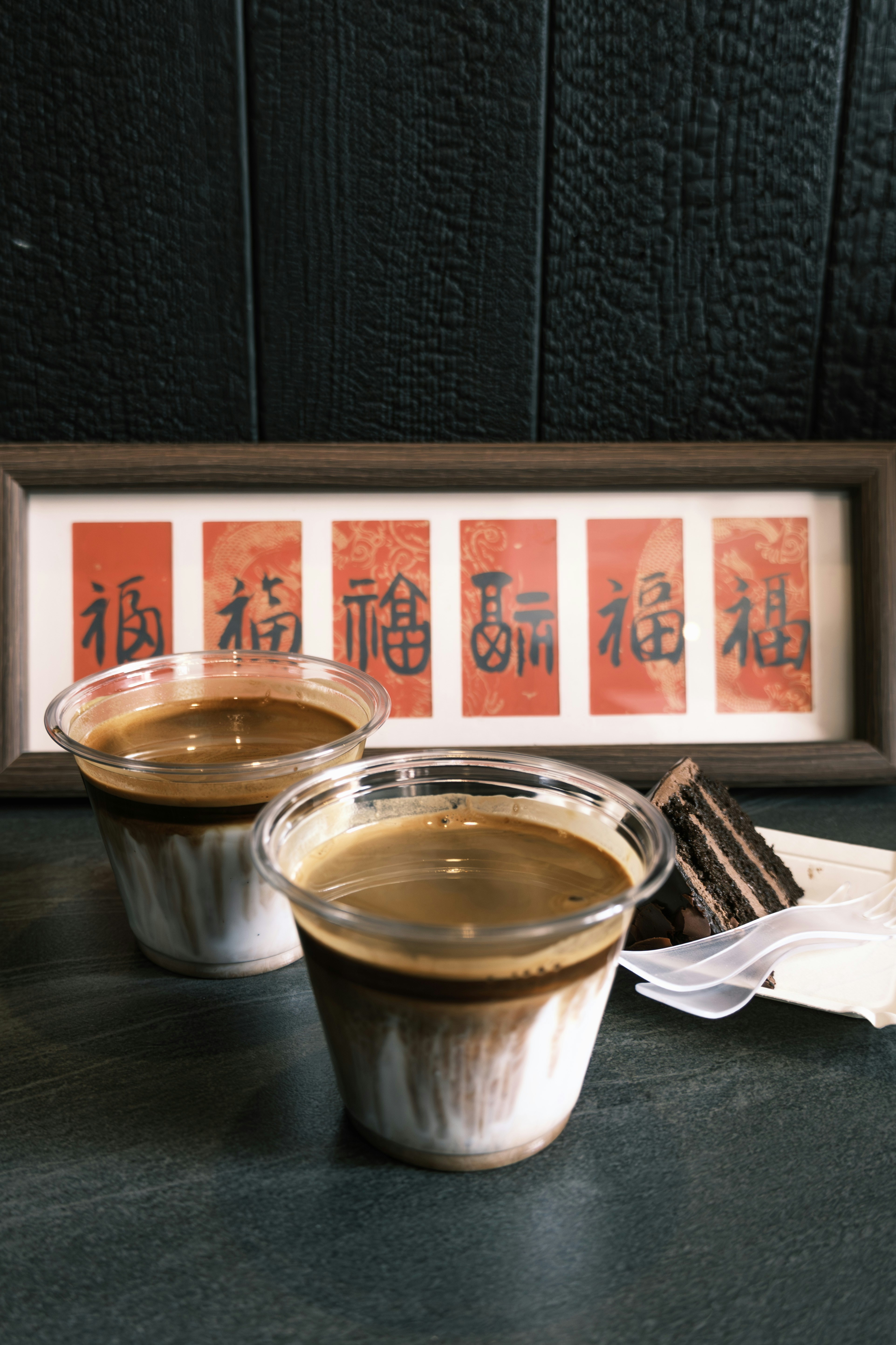 Two coffee cups in foreground with framed red calligraphy artwork in the background
