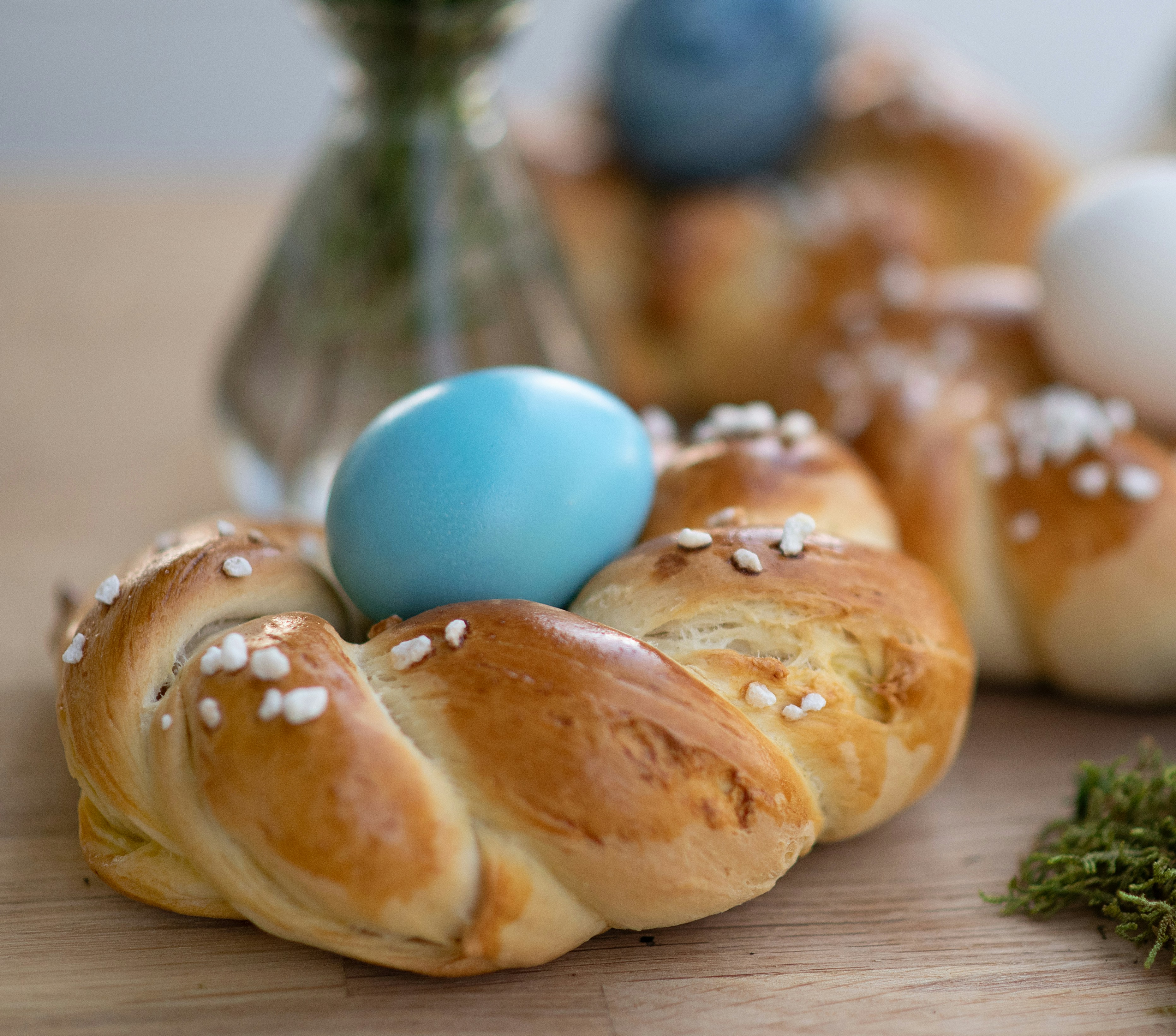 A braided pastry sits on a wooden surface with a blue egg nestled in its center, spotlighting an Easter-inspired arrangement. Note: this is a still-life photo of baked goods and a dyed egg.