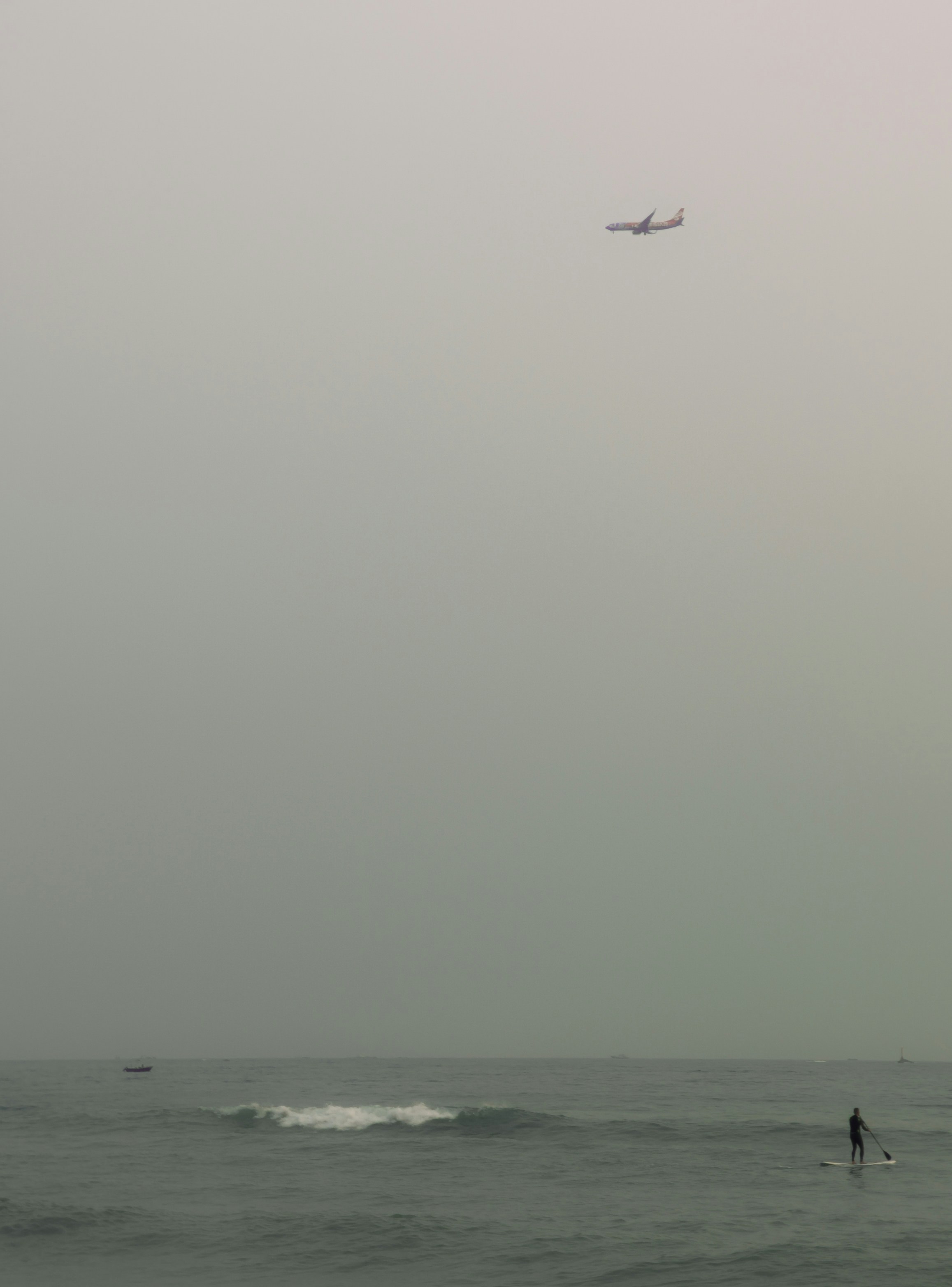 Soaring Alone: A distant plane against pastel coastal haze