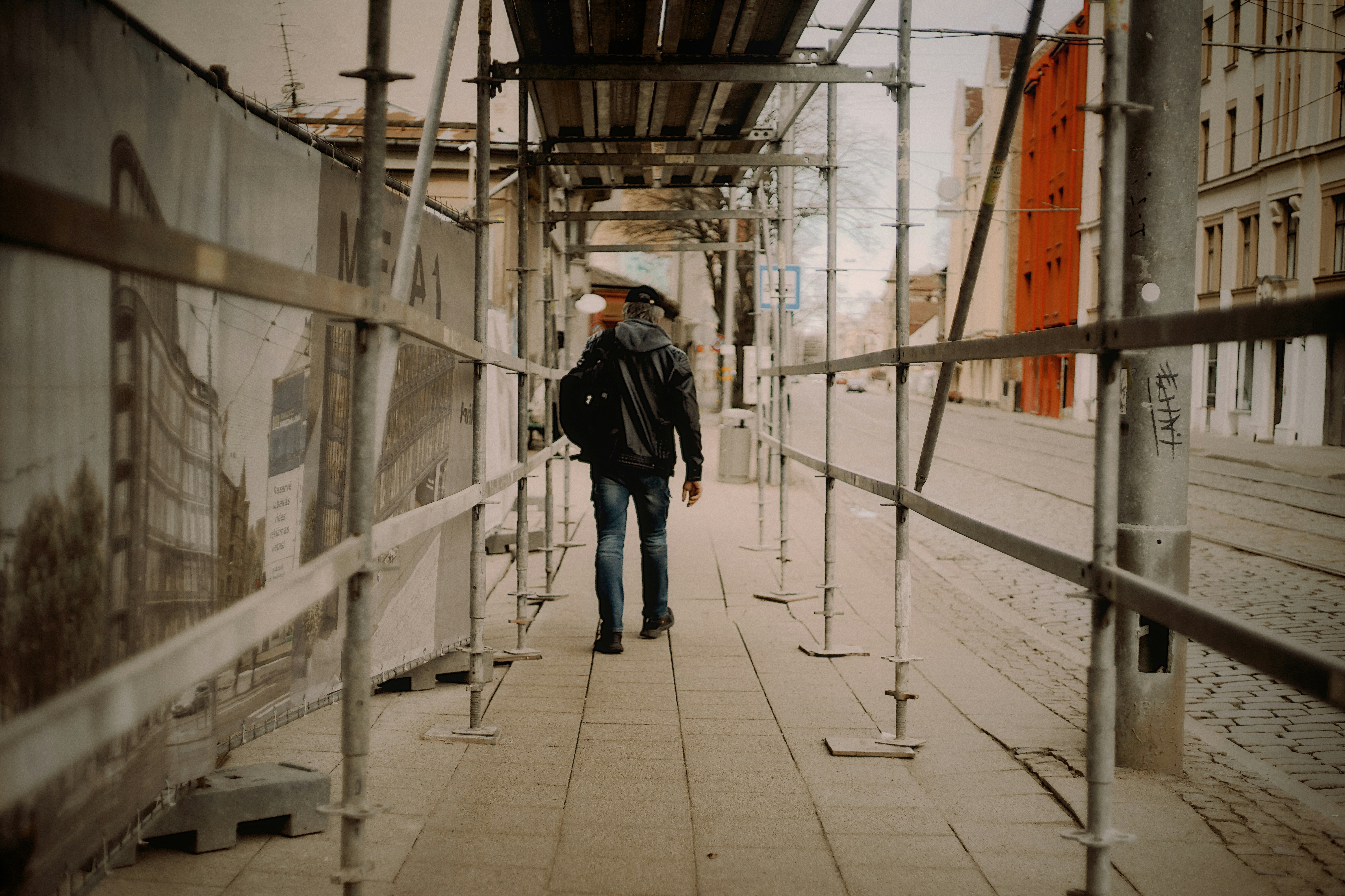 Walking the Seamed Street: A Solo Figure Beneath Scaffolding