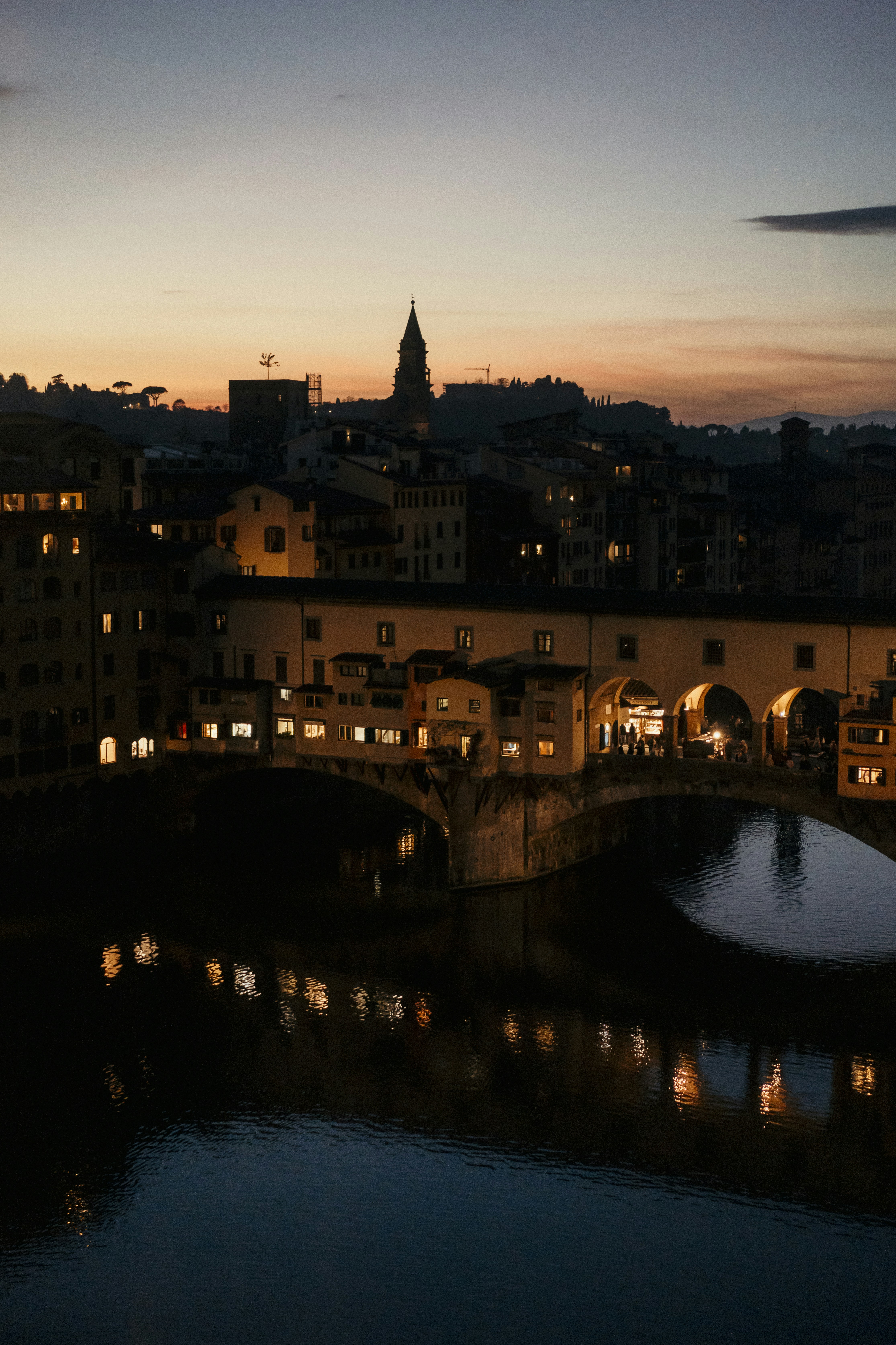  twilight over the Ponte Vecchio—warm lights along the arches and a distant church spire