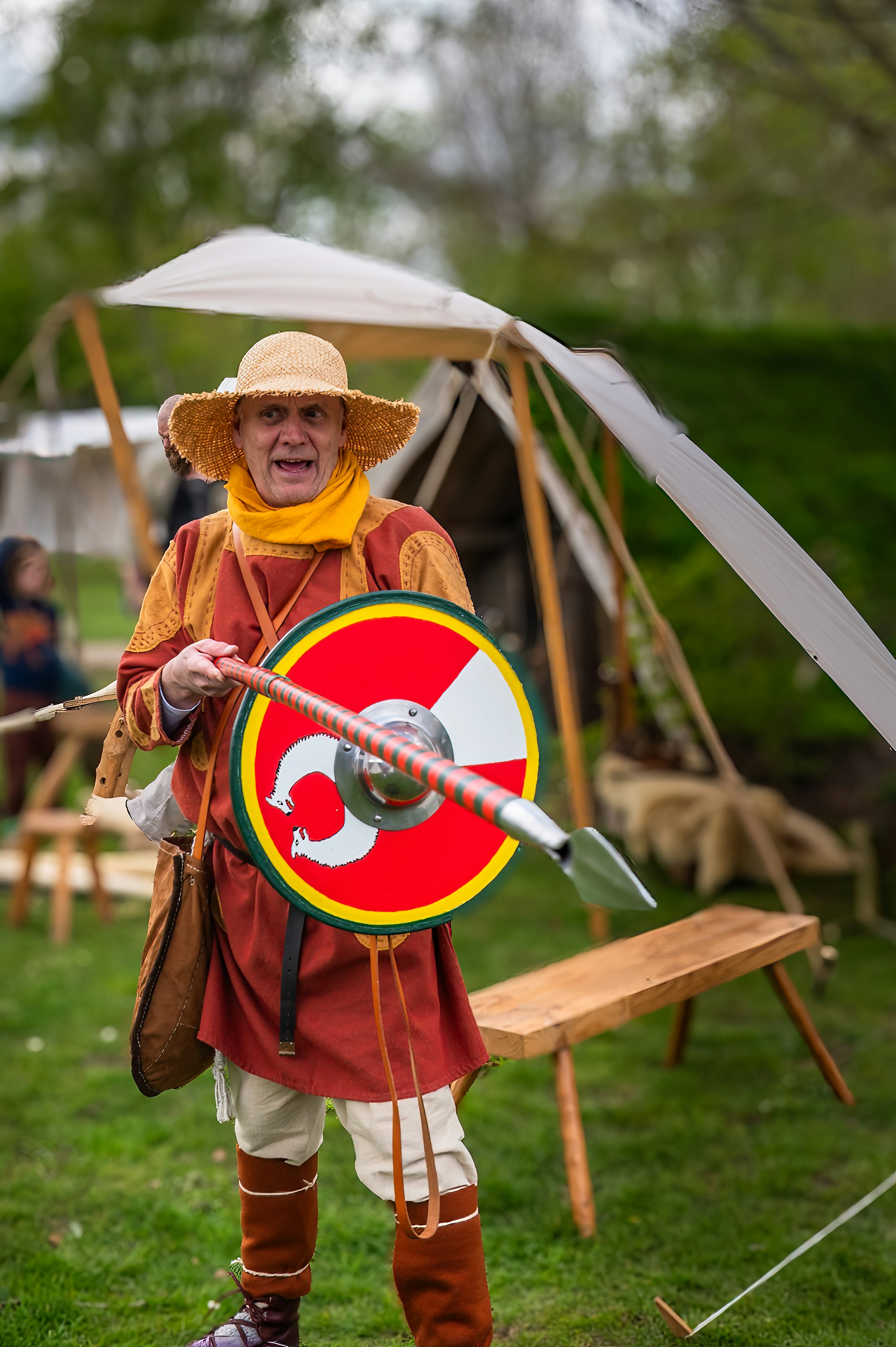 Medieval reenactor with shield and spear in a grassy camp