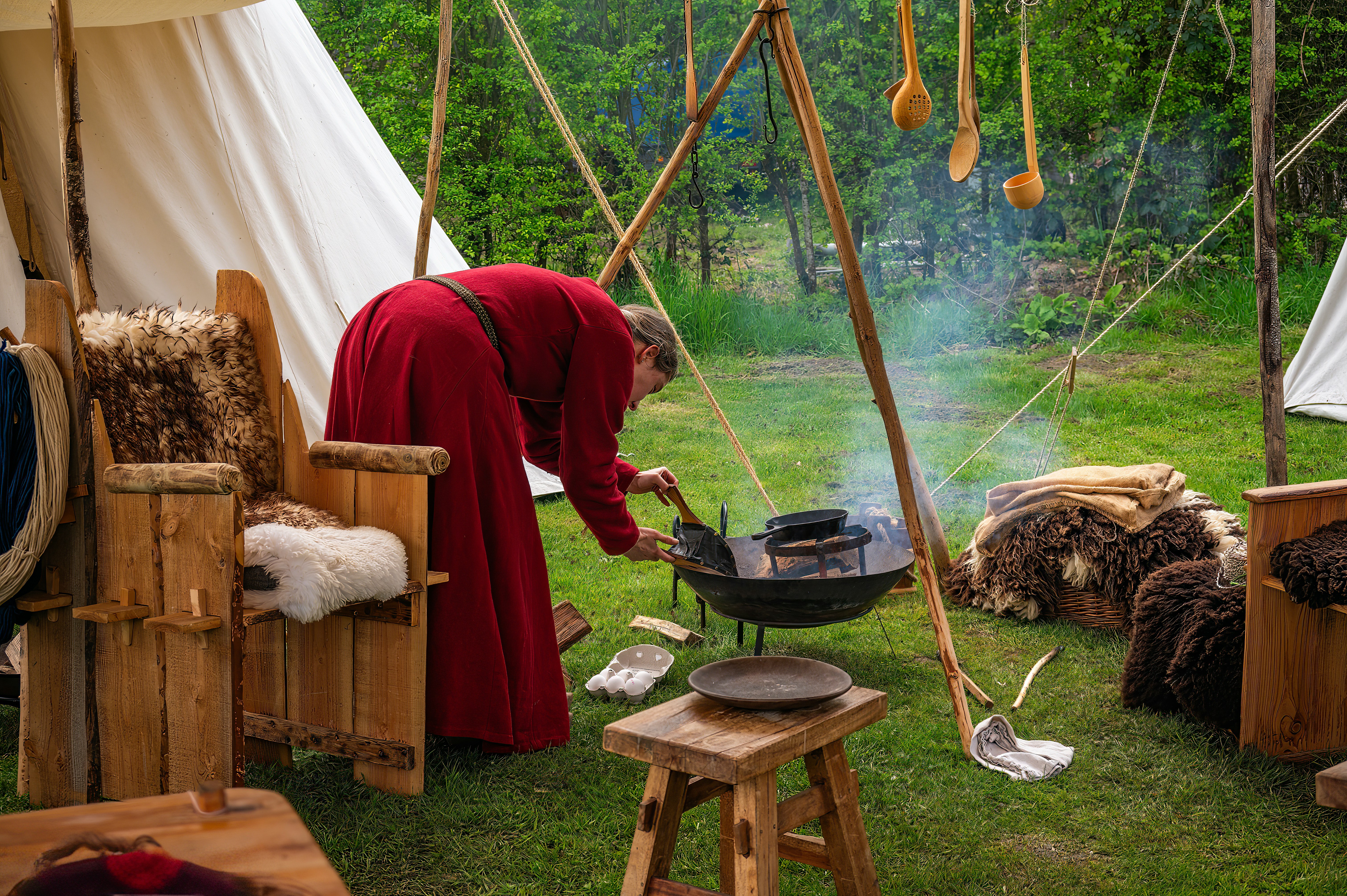 Red-clad cook tending a campfire in a rustic encampment