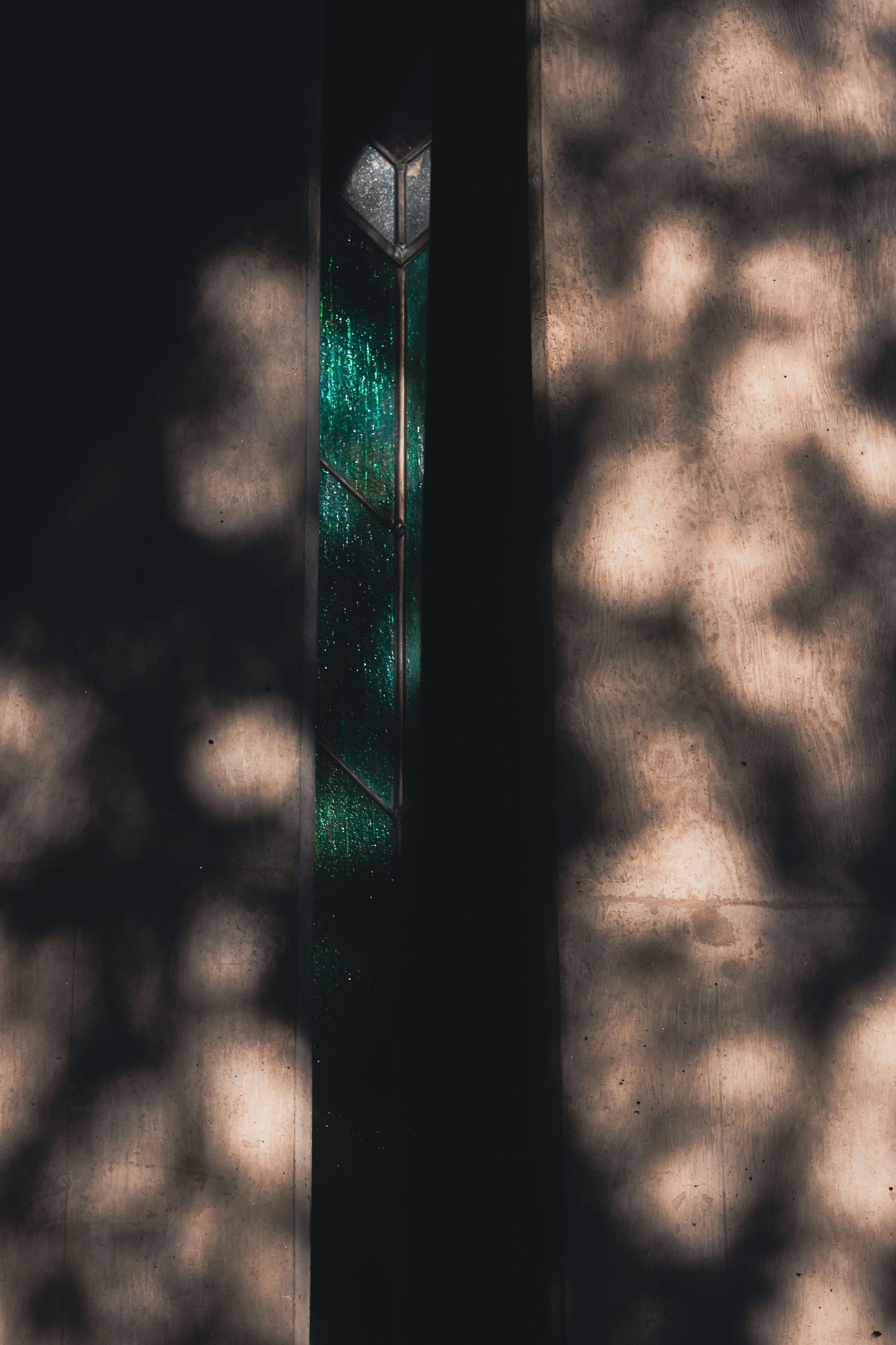 Slim vertical window channel catching green light through a rain-streaked glass