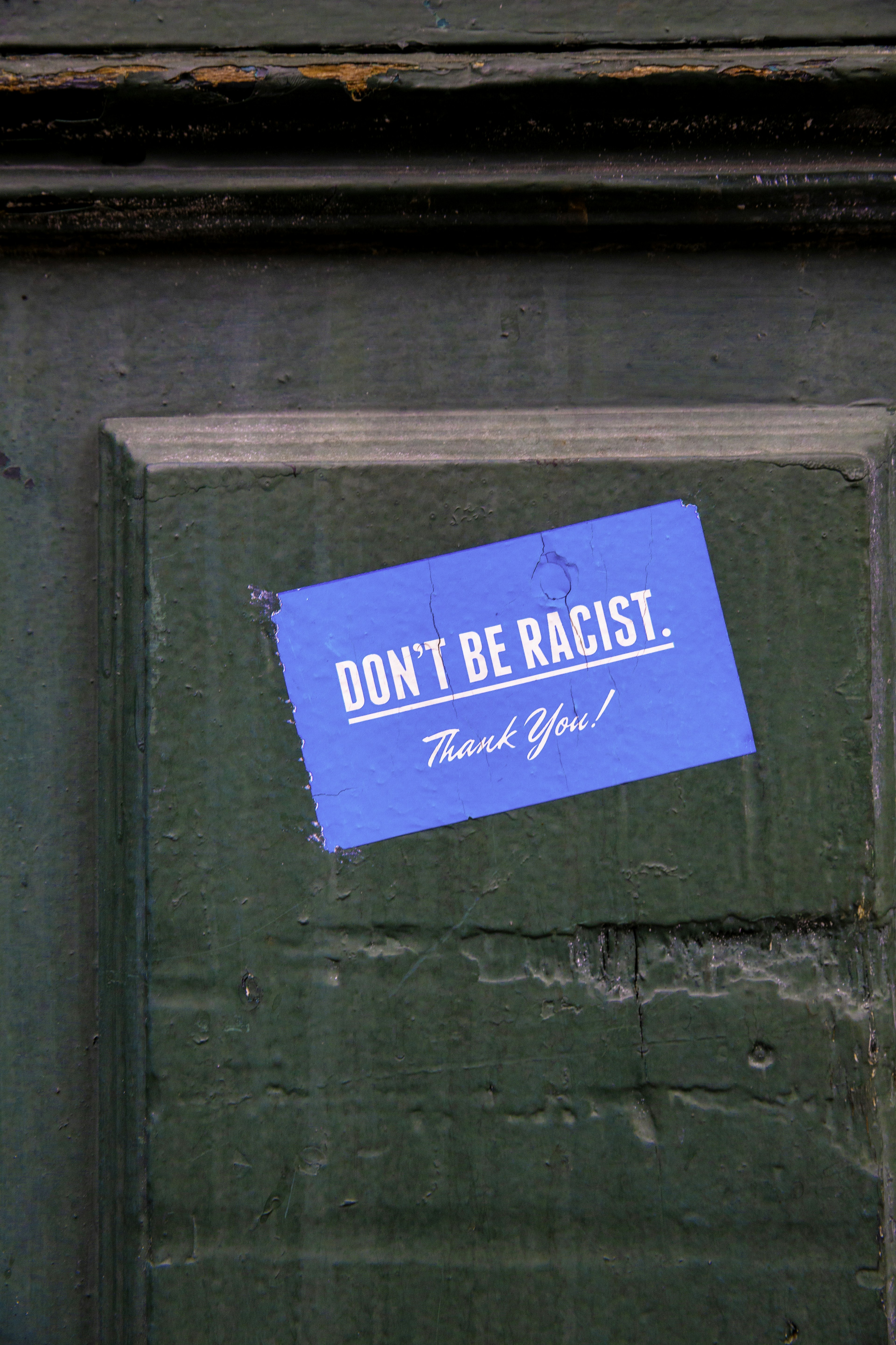 Blue sticker with 'DON'T BE RACIST' on a weathered green door