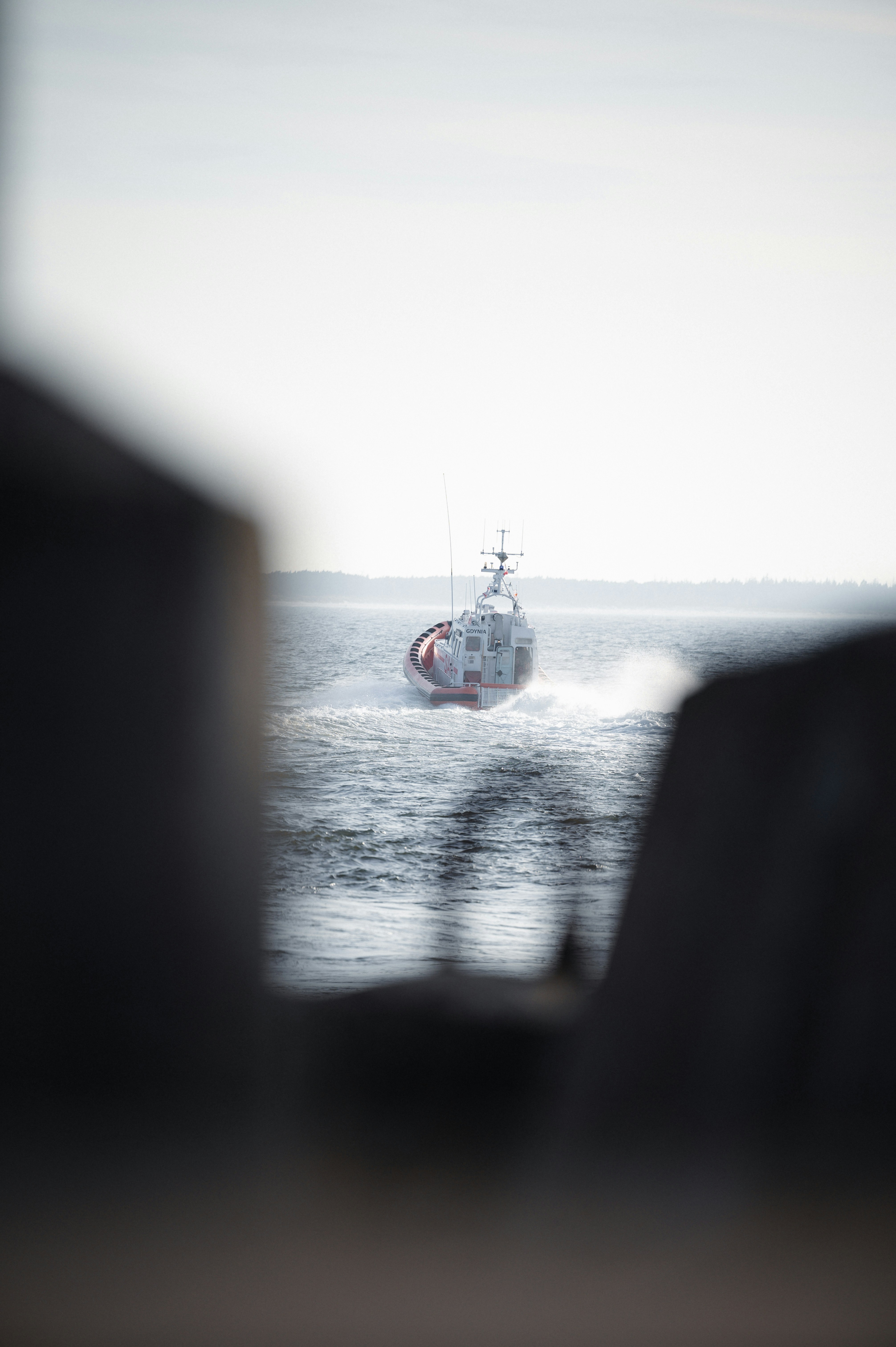 A Vessel Emerges from the Gap Between Shadowed Breakwaters