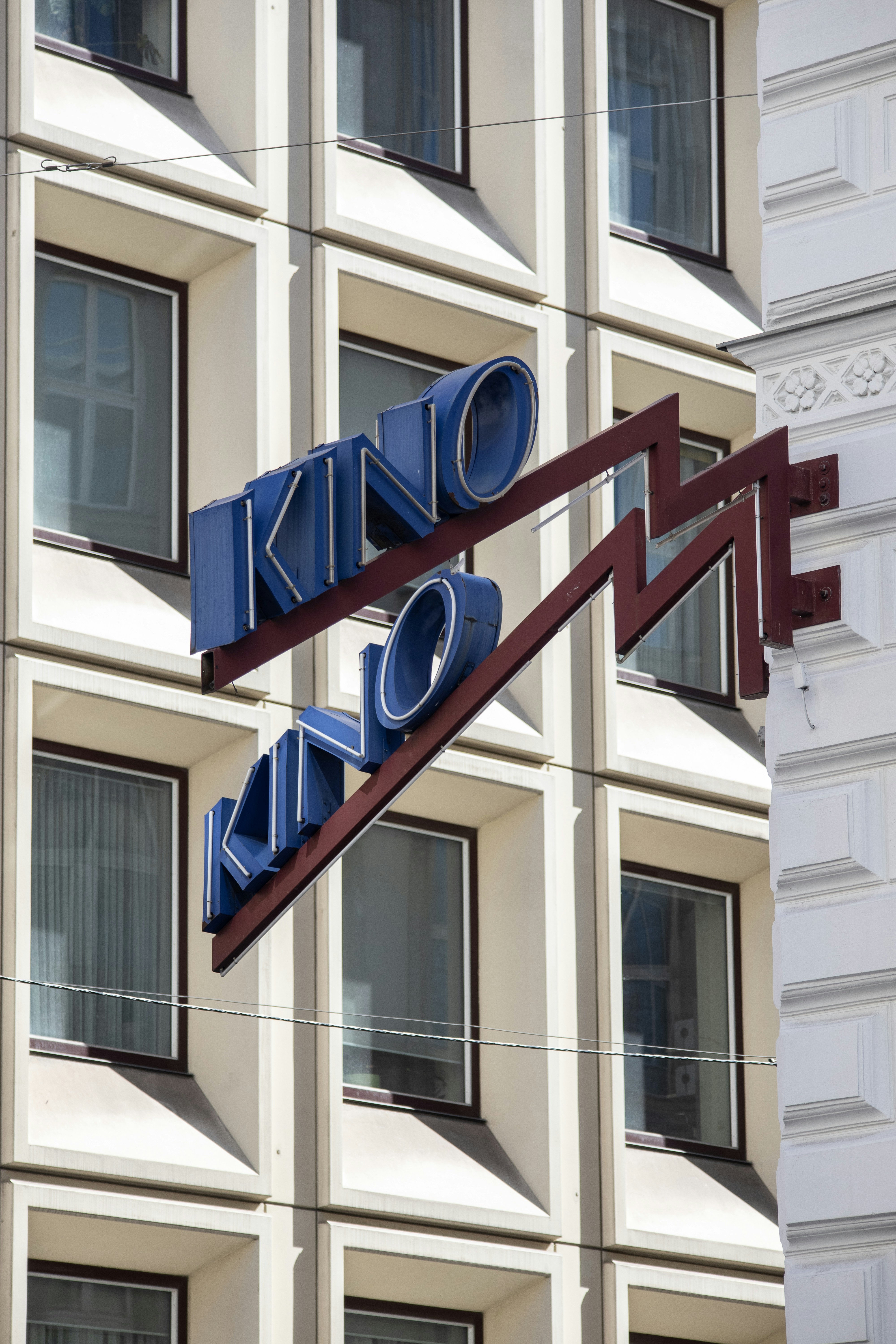 Blue Neon Kinom Sign Cuts Across a Sunlit Urban Facade