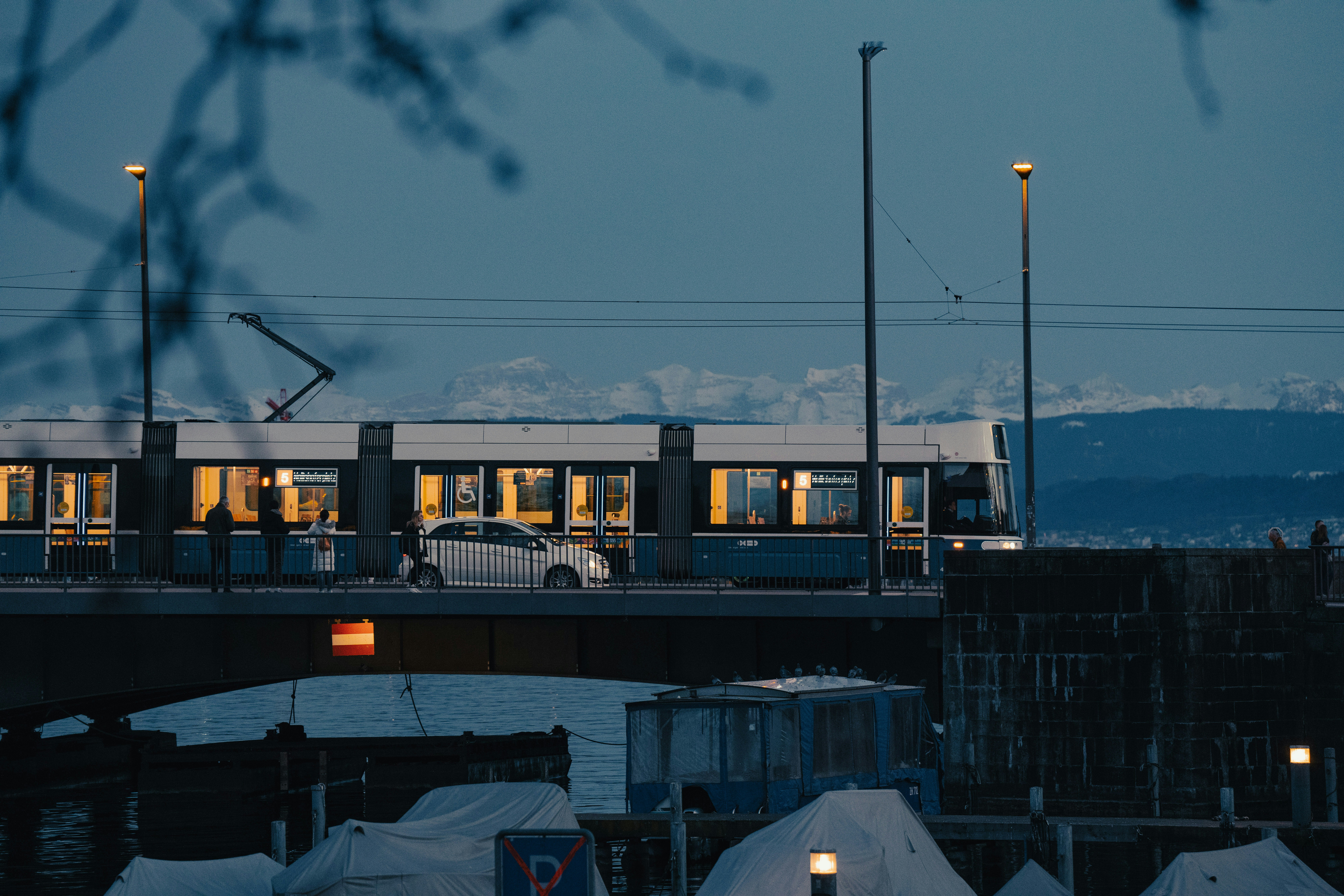 Commuter tram at dusk: lights glow on a suspended city bridge
