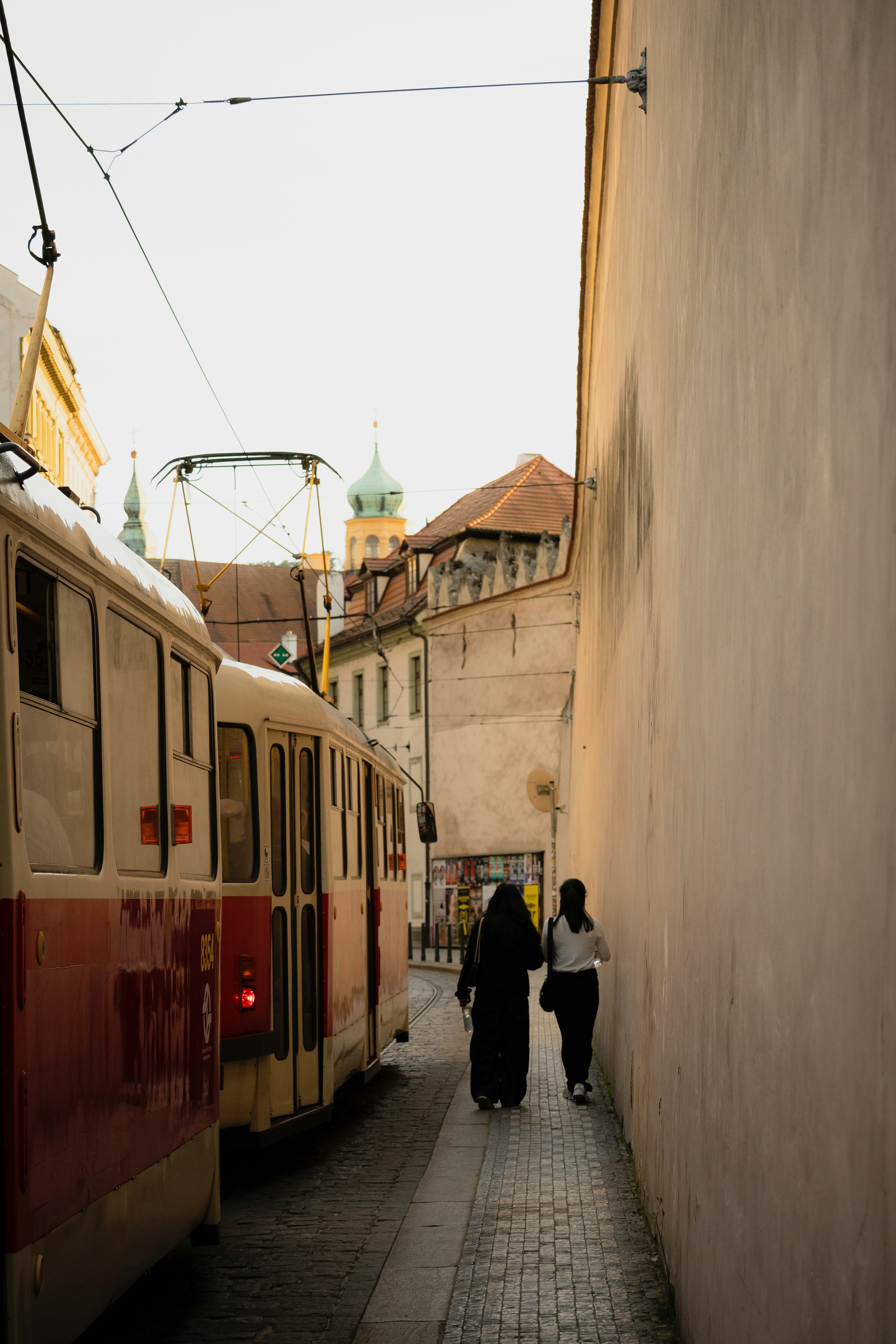 Narrow Streetcar Corridor: Two pedestrians in a sunlit alley flanked by a waiting tram