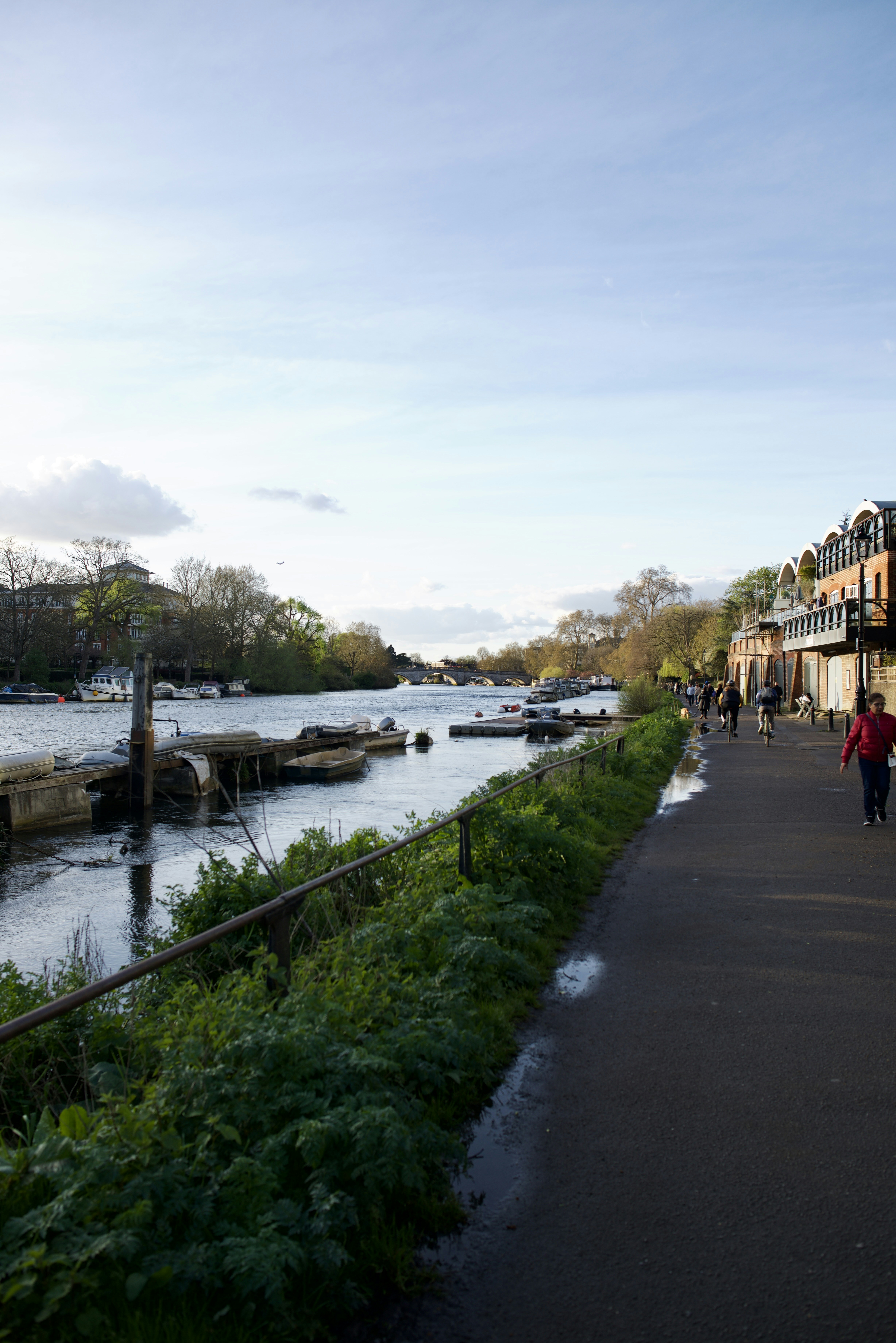 Riverside Promenade: Boats, Brick Facades, and Evening Walkers