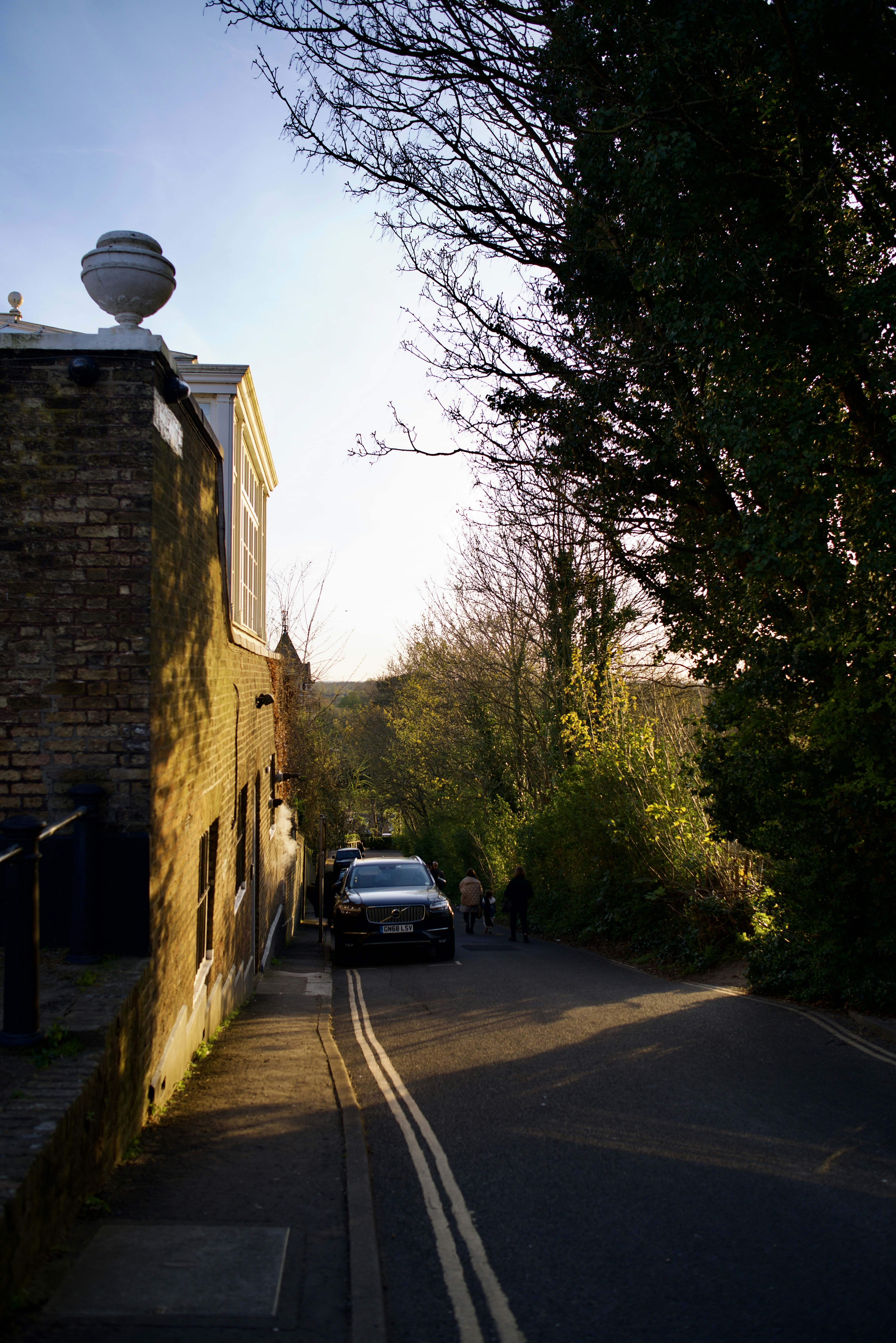 Sunlit Street Corridor: Car, Pedestrians, and Verdant Curve